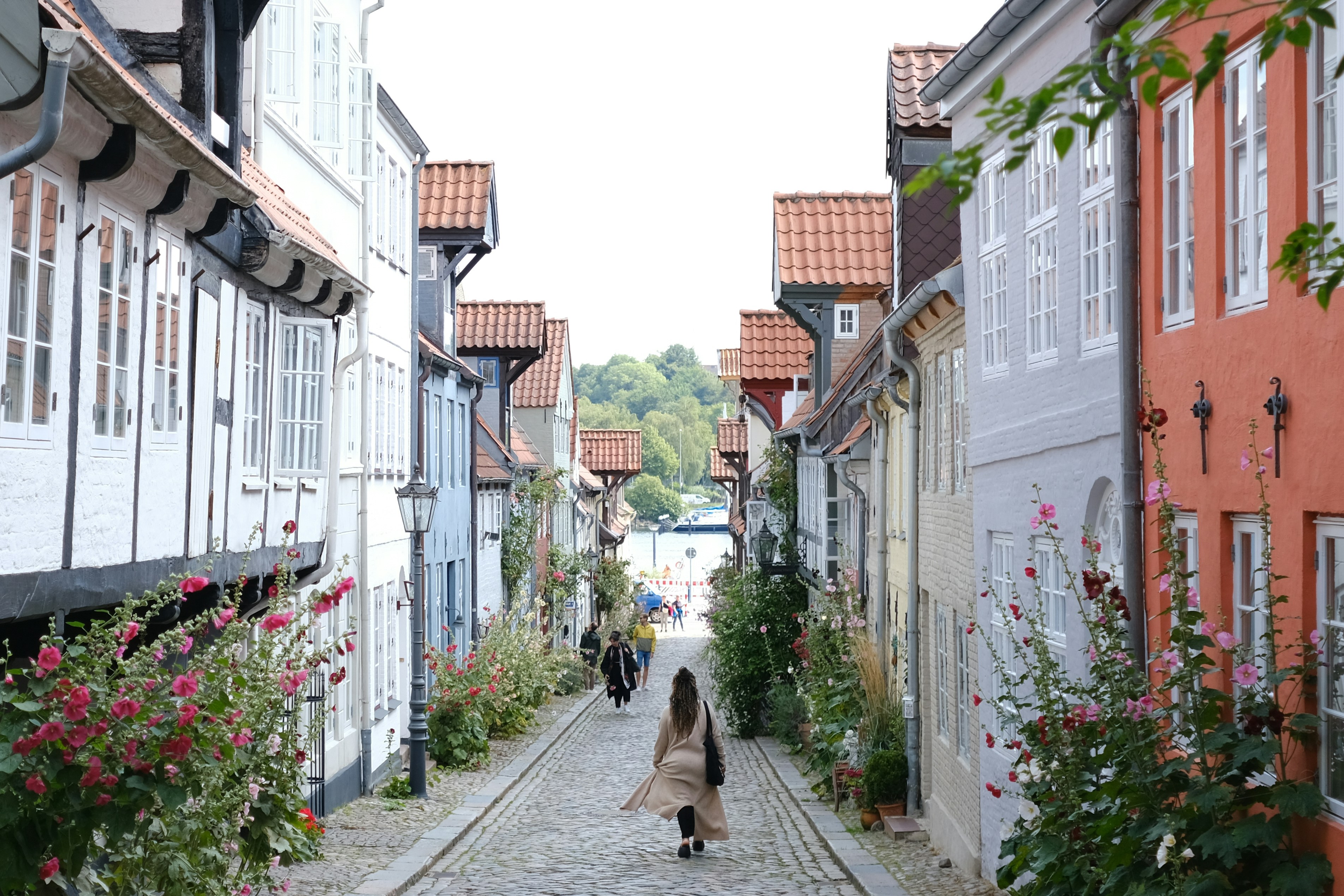 Woman walking down a narrow cobblestone street lined with colorful historic buildings and blooming flowers.