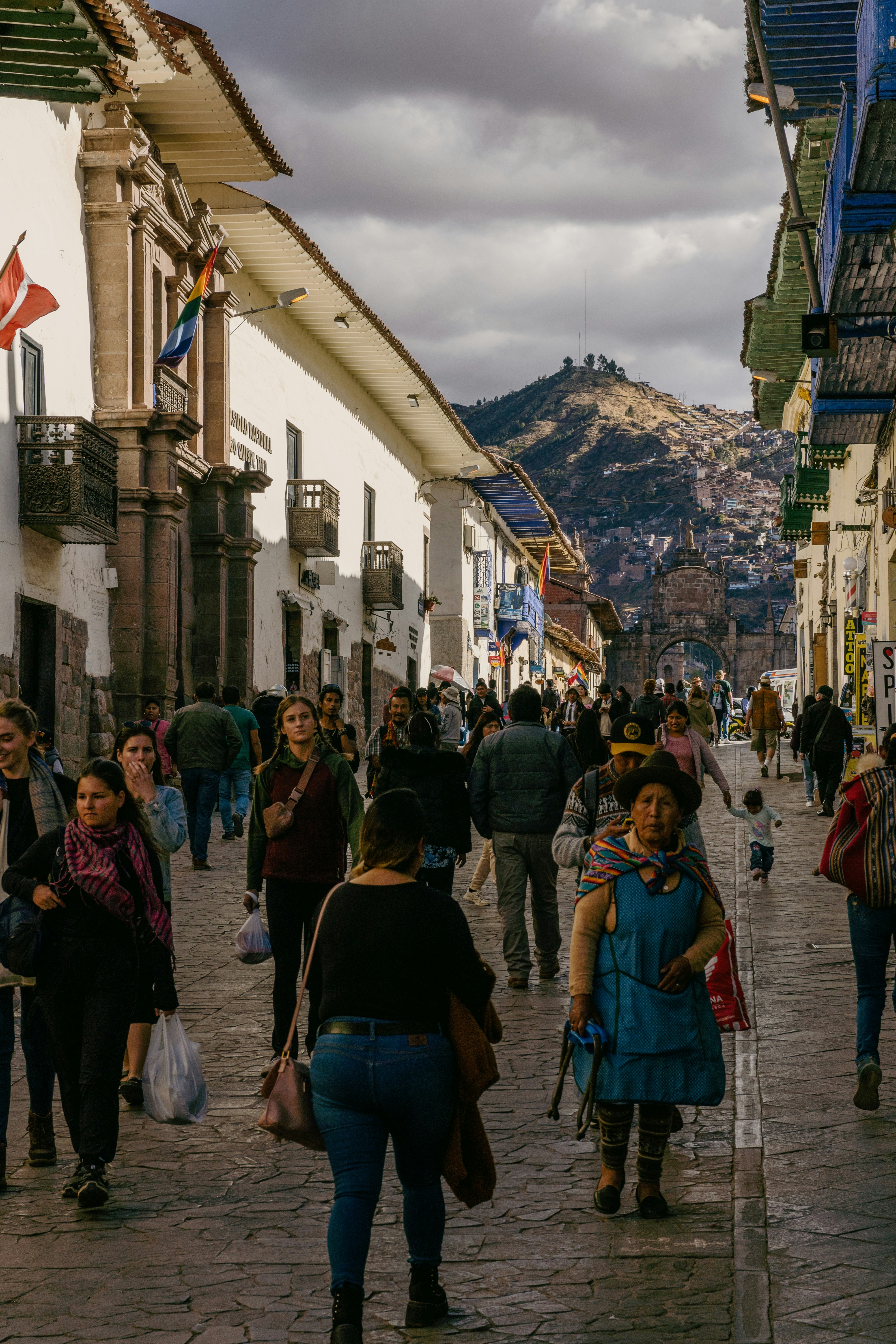 Blue-Dressed Vendor Framed by a Crowded Colonial Calle toward a Mountain Gate