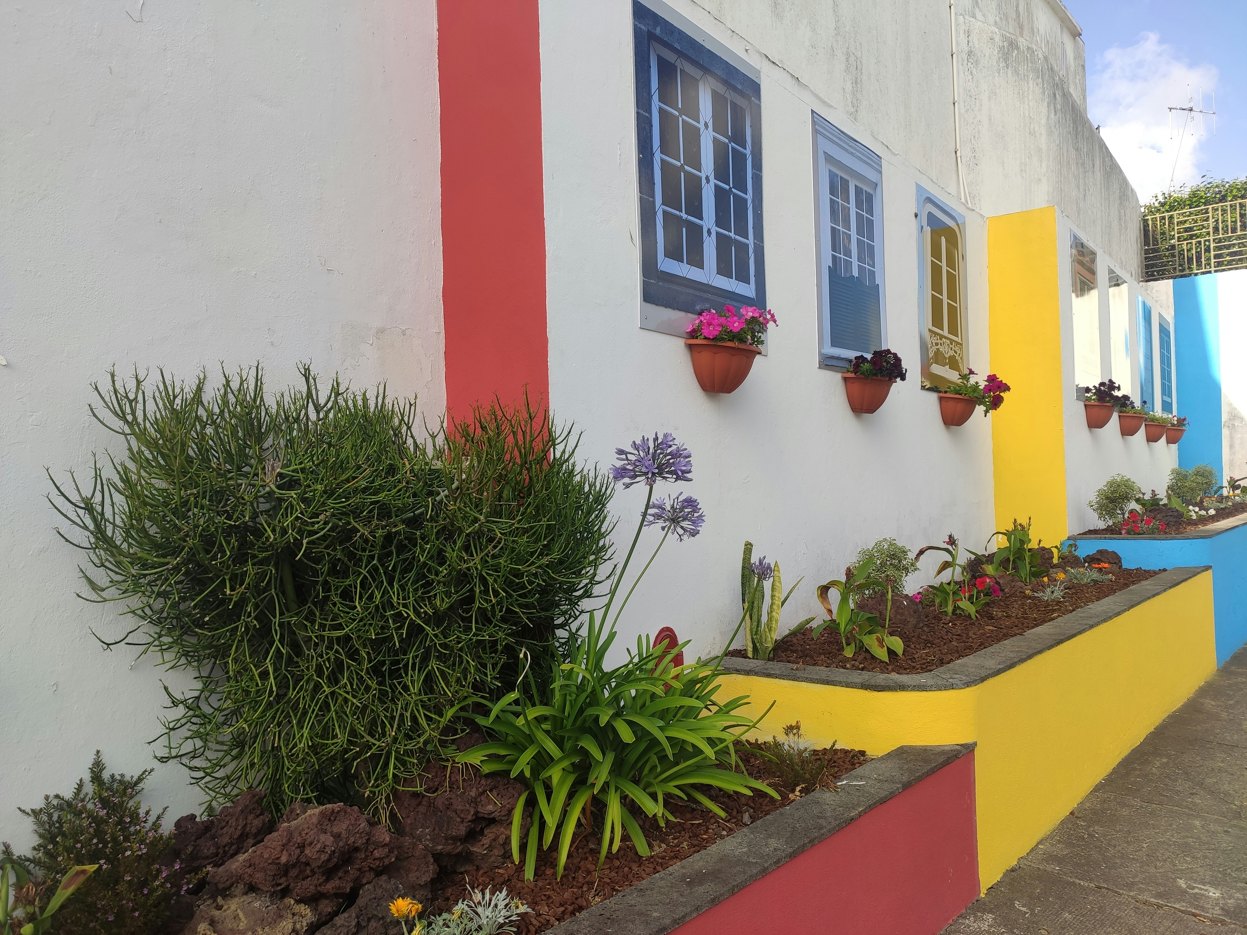 Colorful flower boxes adorn a white building with red, blue, and yellow accents.