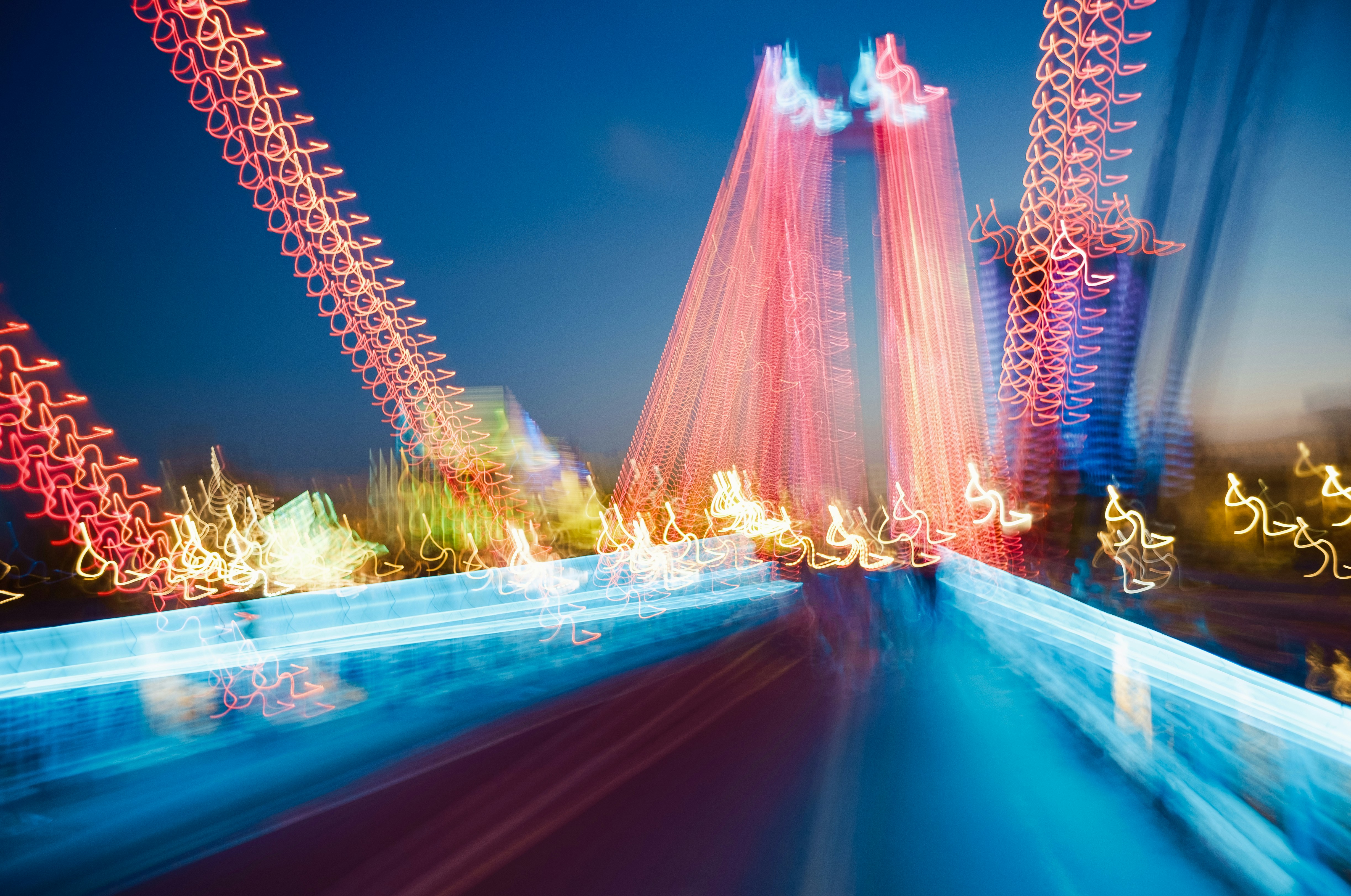 Vivid light trails create abstract patterns over a bridge at night.