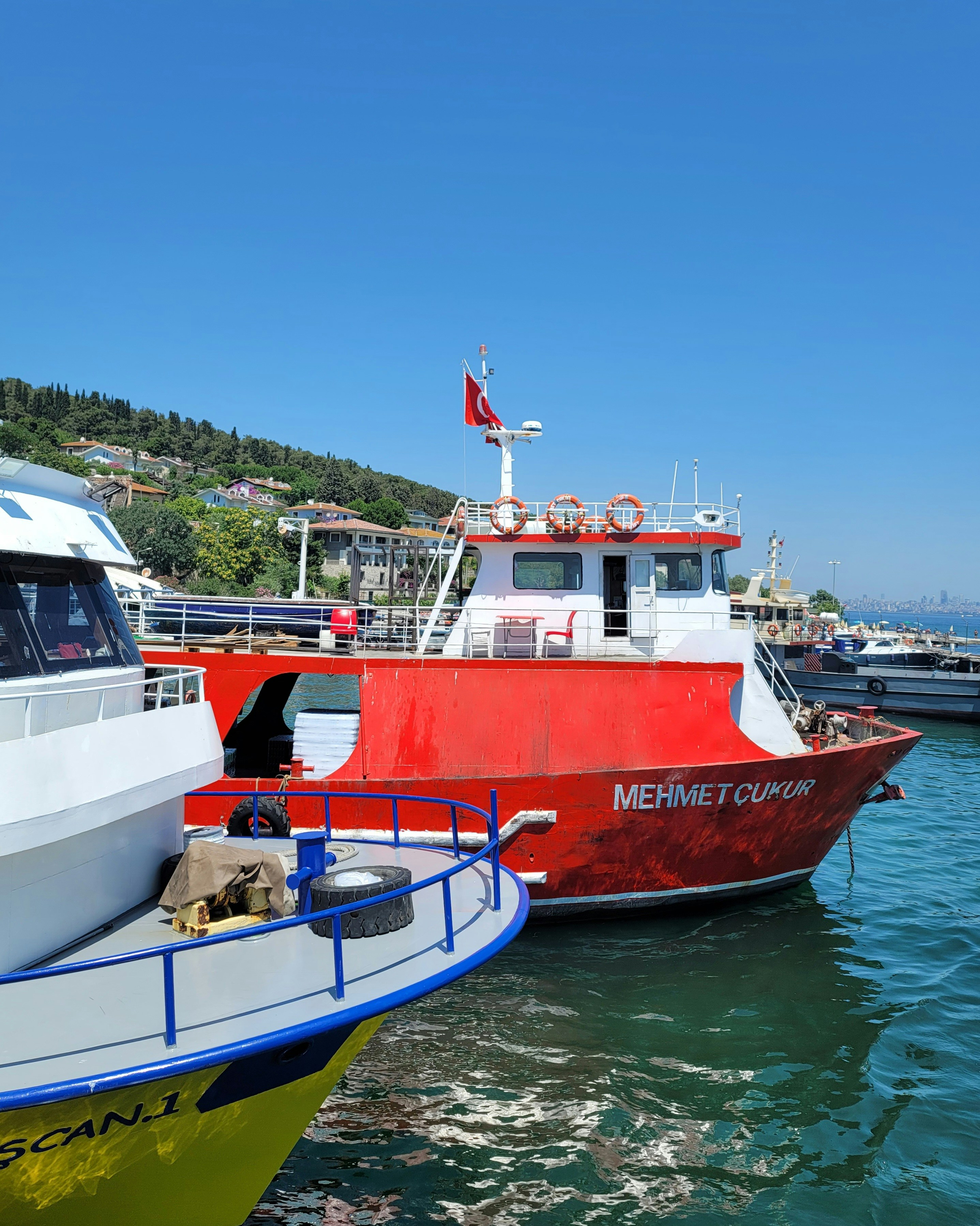 Red-hulled vessel docks in a sunlit Turkish harbor