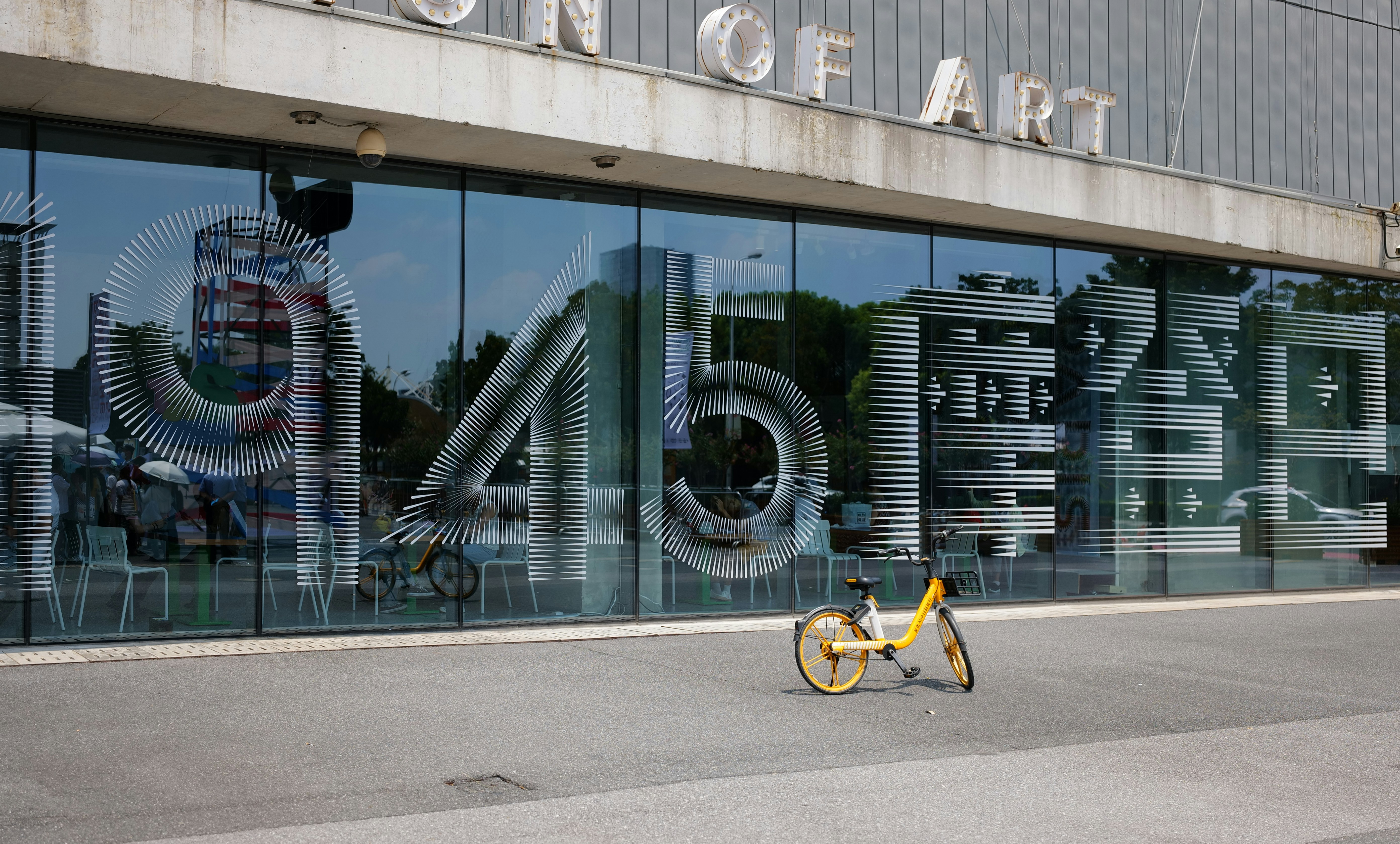Bright yellow bicycle sits in front of a glass storefront displaying oversized numeric art.