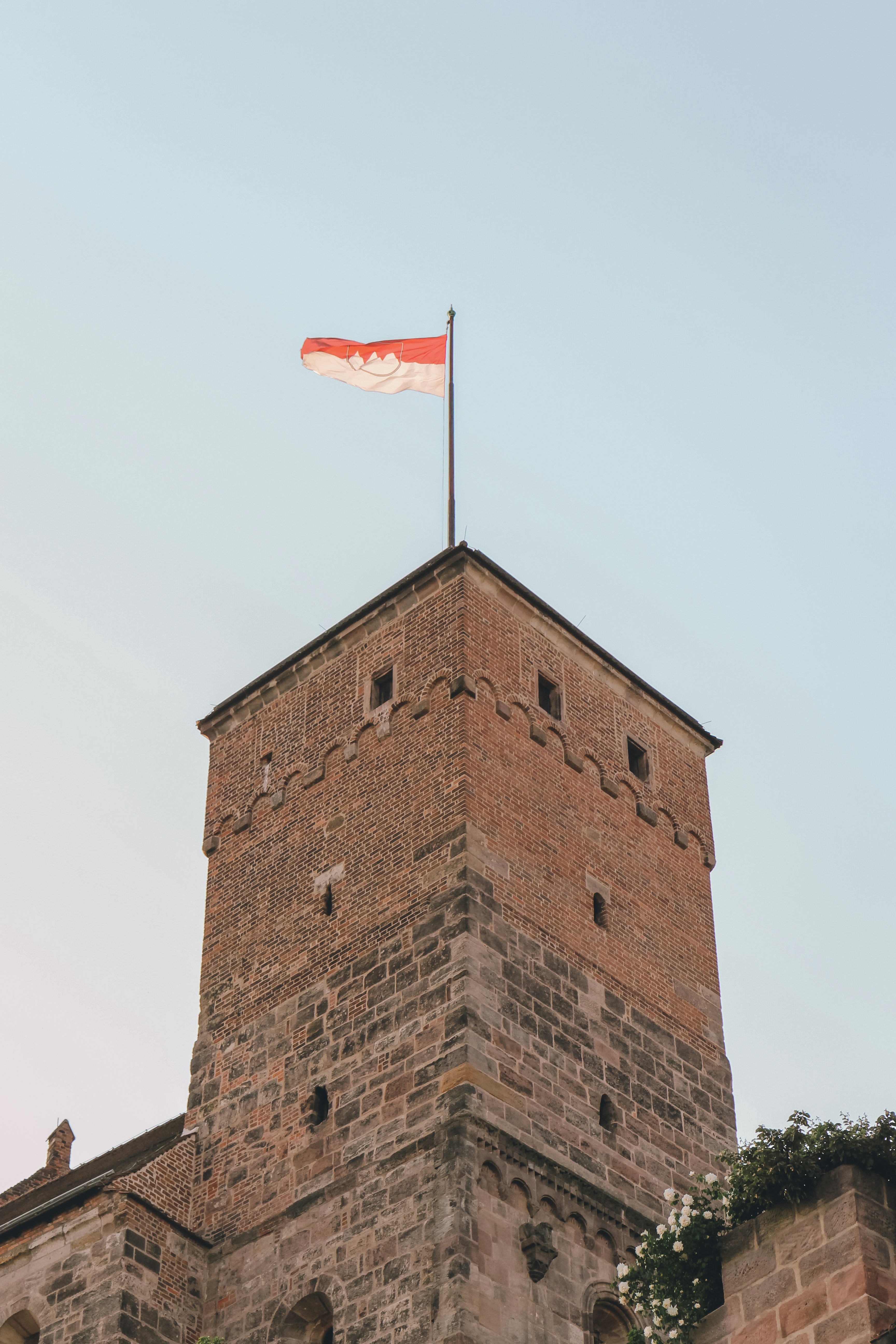 Flag atop a medieval brick turret, framed by a calm blue sky