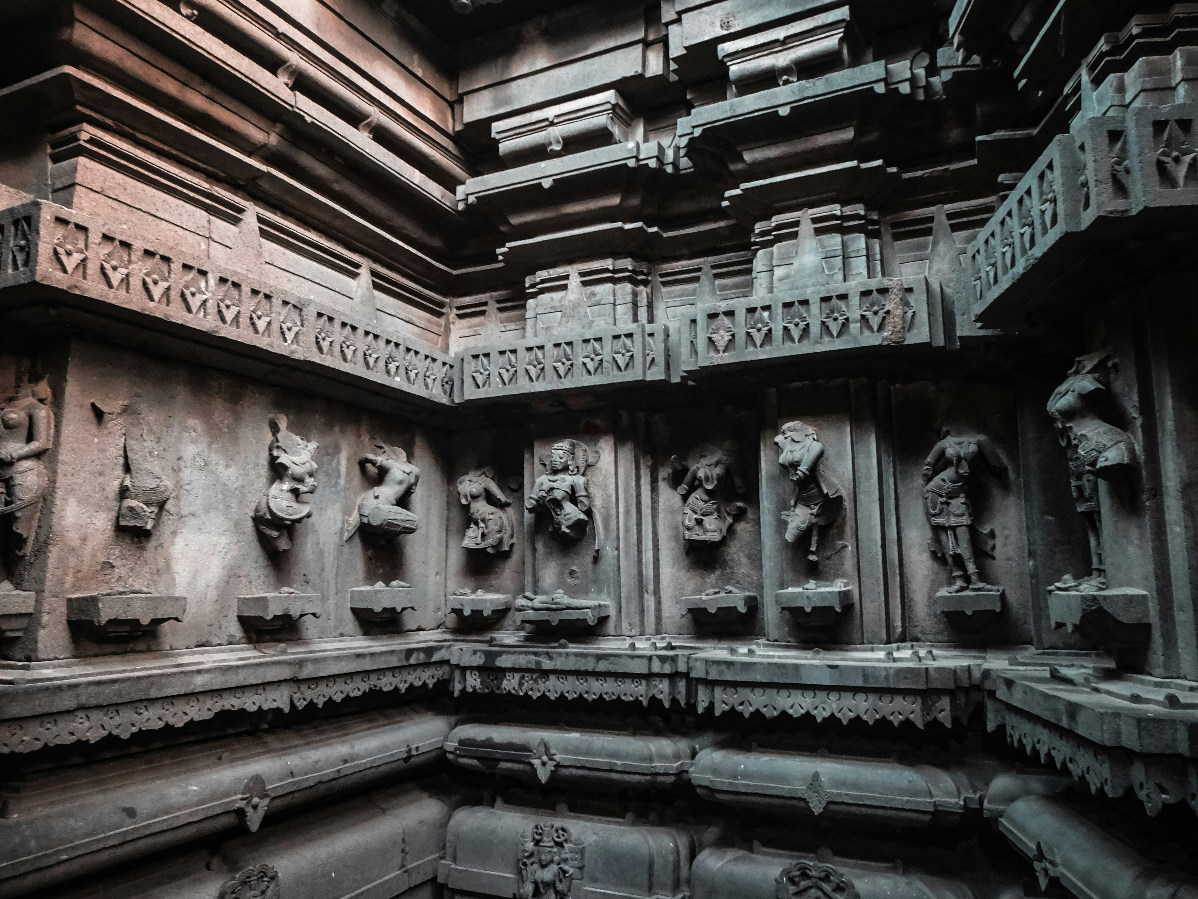 Photograph of a temple wall lined with carved figures and decorative friezes along a layered stone corridor.