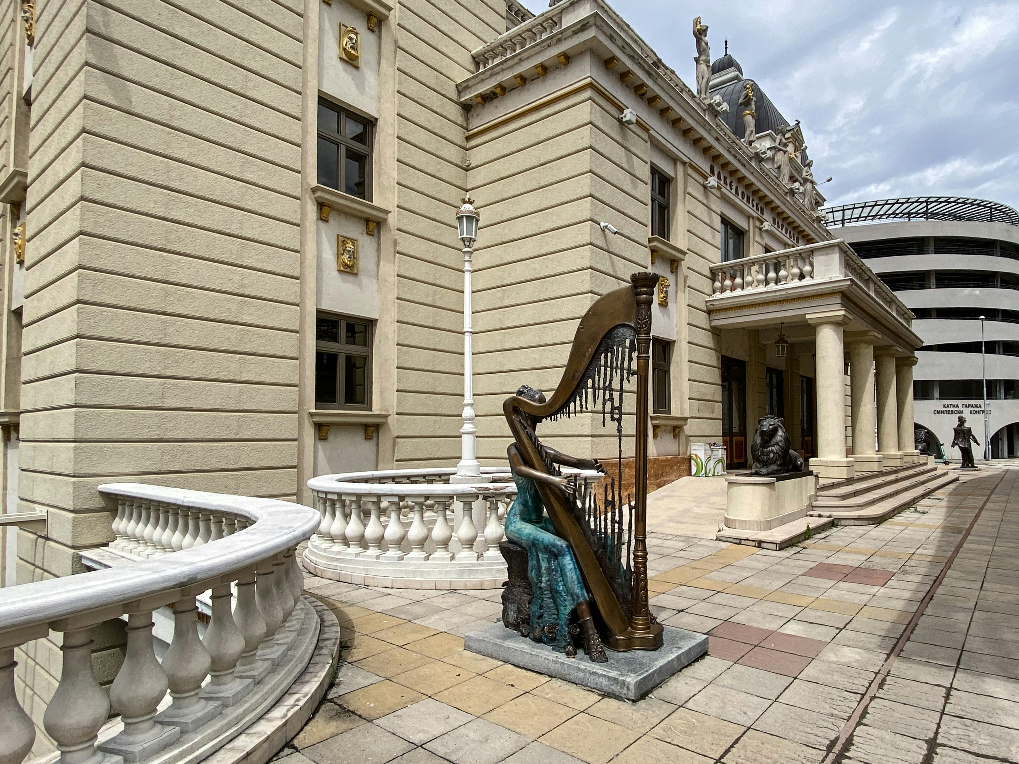 A bronze harp sculpture graces the entrance of a grand building, blending artistic expression with architectural design. The scene captures a unique interplay of light and shadow.