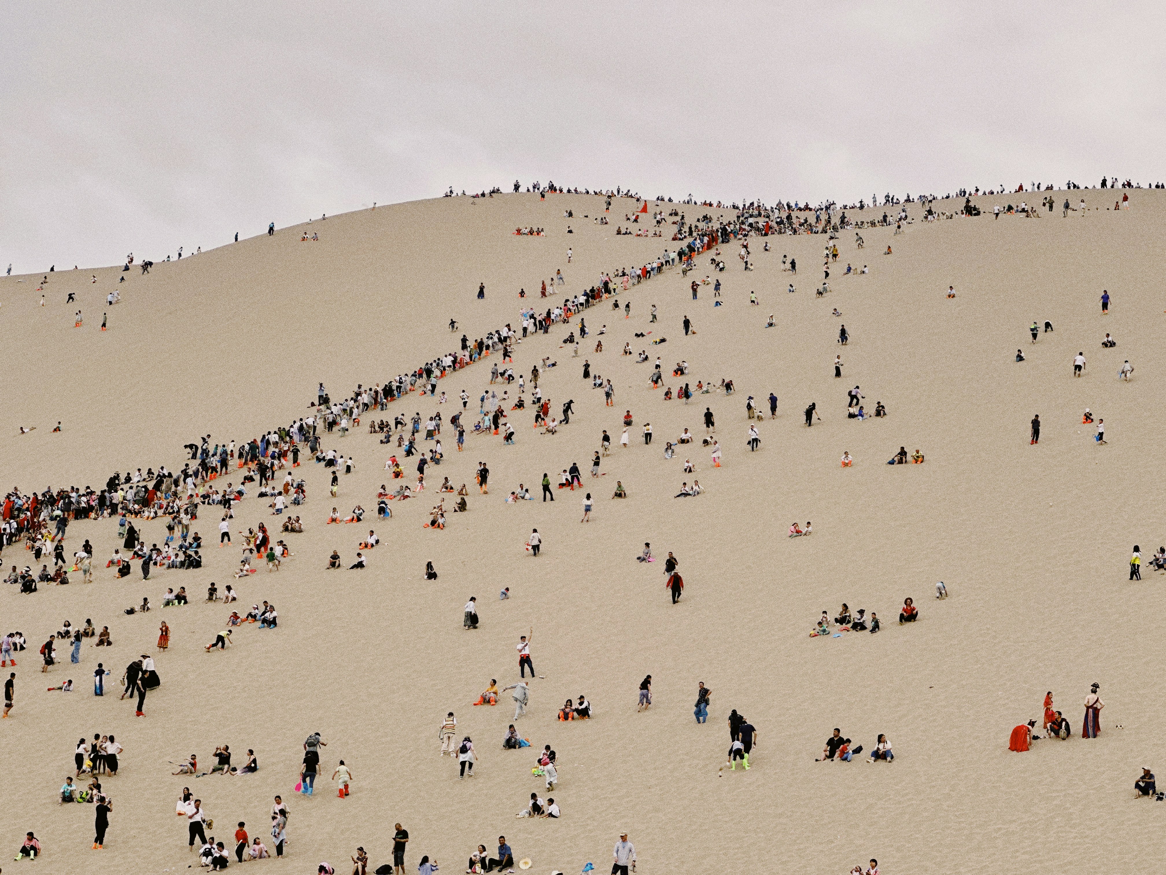 Ridge of Footsteps: Crowds Trek Across a Quiet Dune
