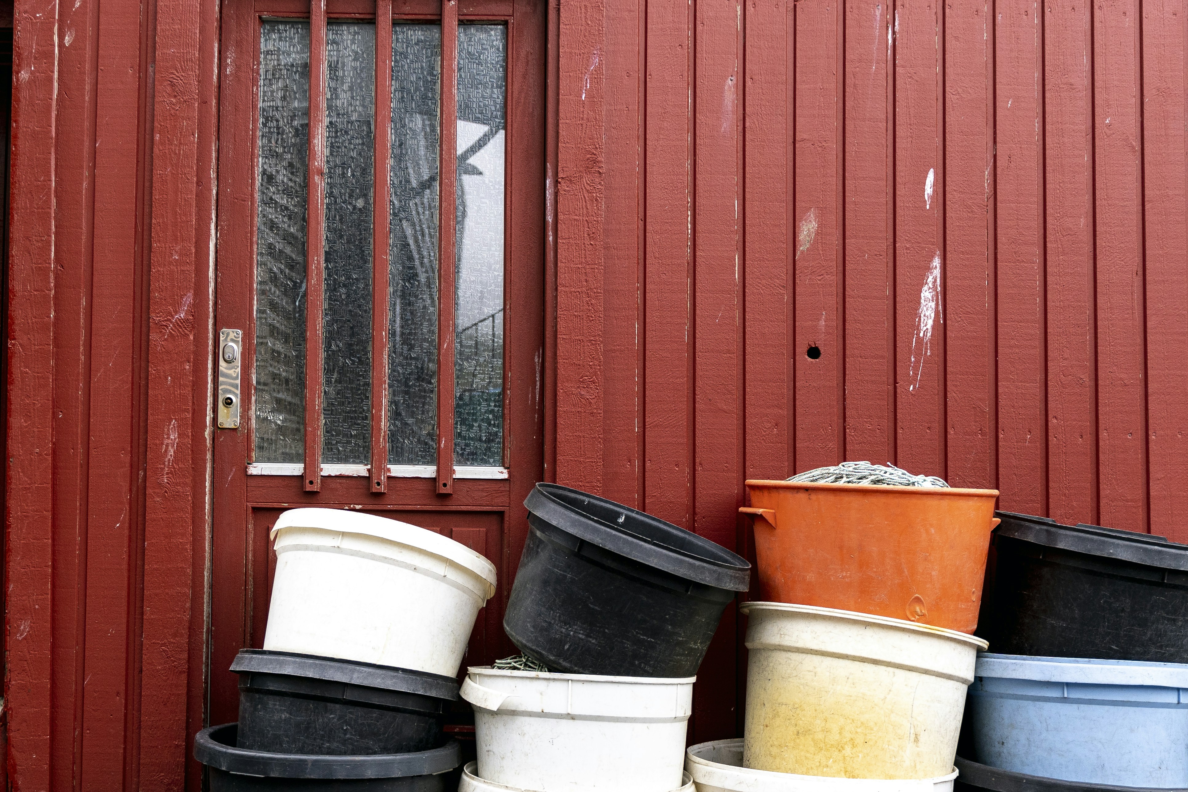 Used buckets in a fishing harbor in the Faroe Islands | a pile of buckets sitting in front of a red building