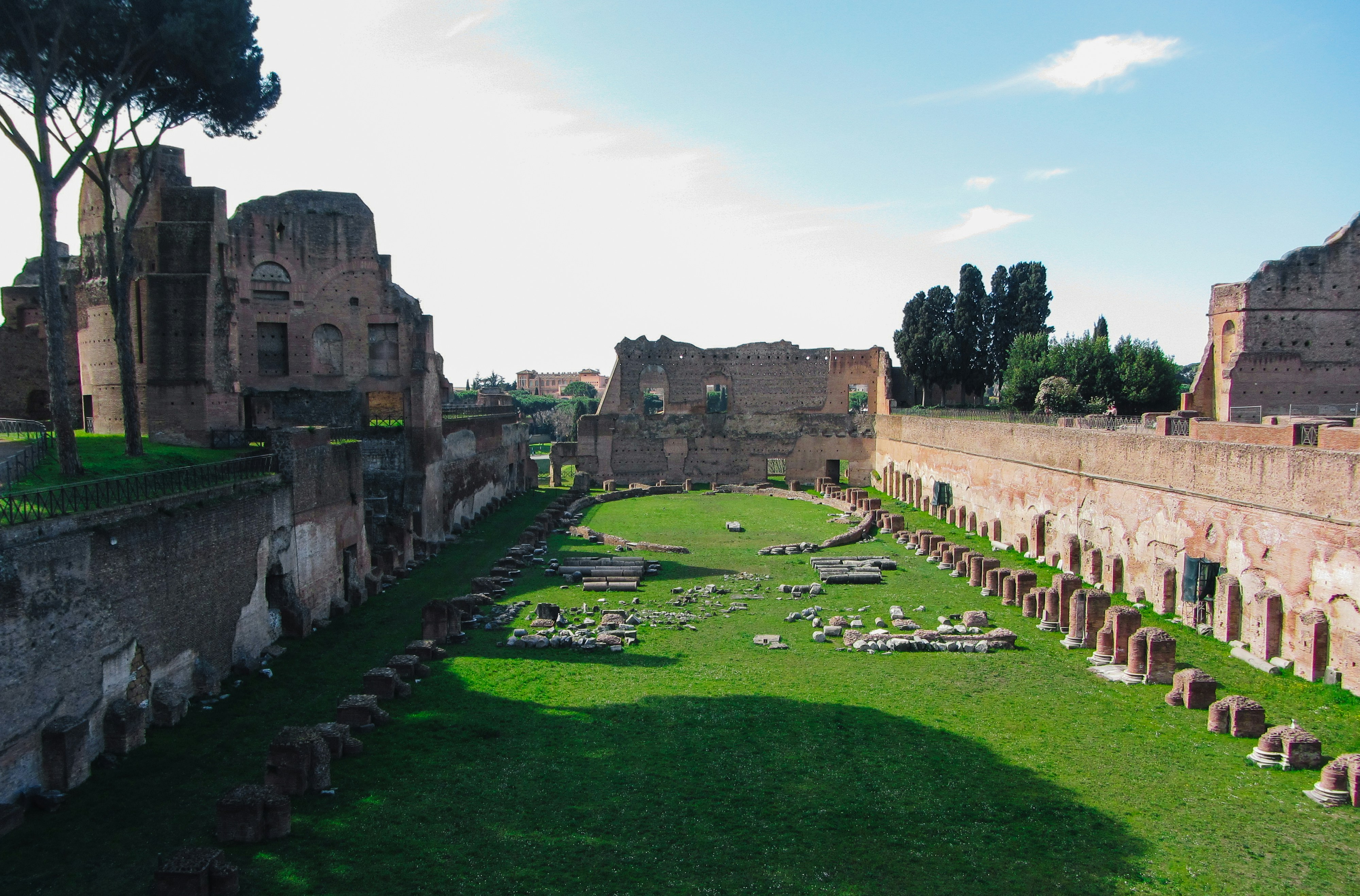 Ruins of an ancient stadium with stone walls and green grass under a clear blue sky.