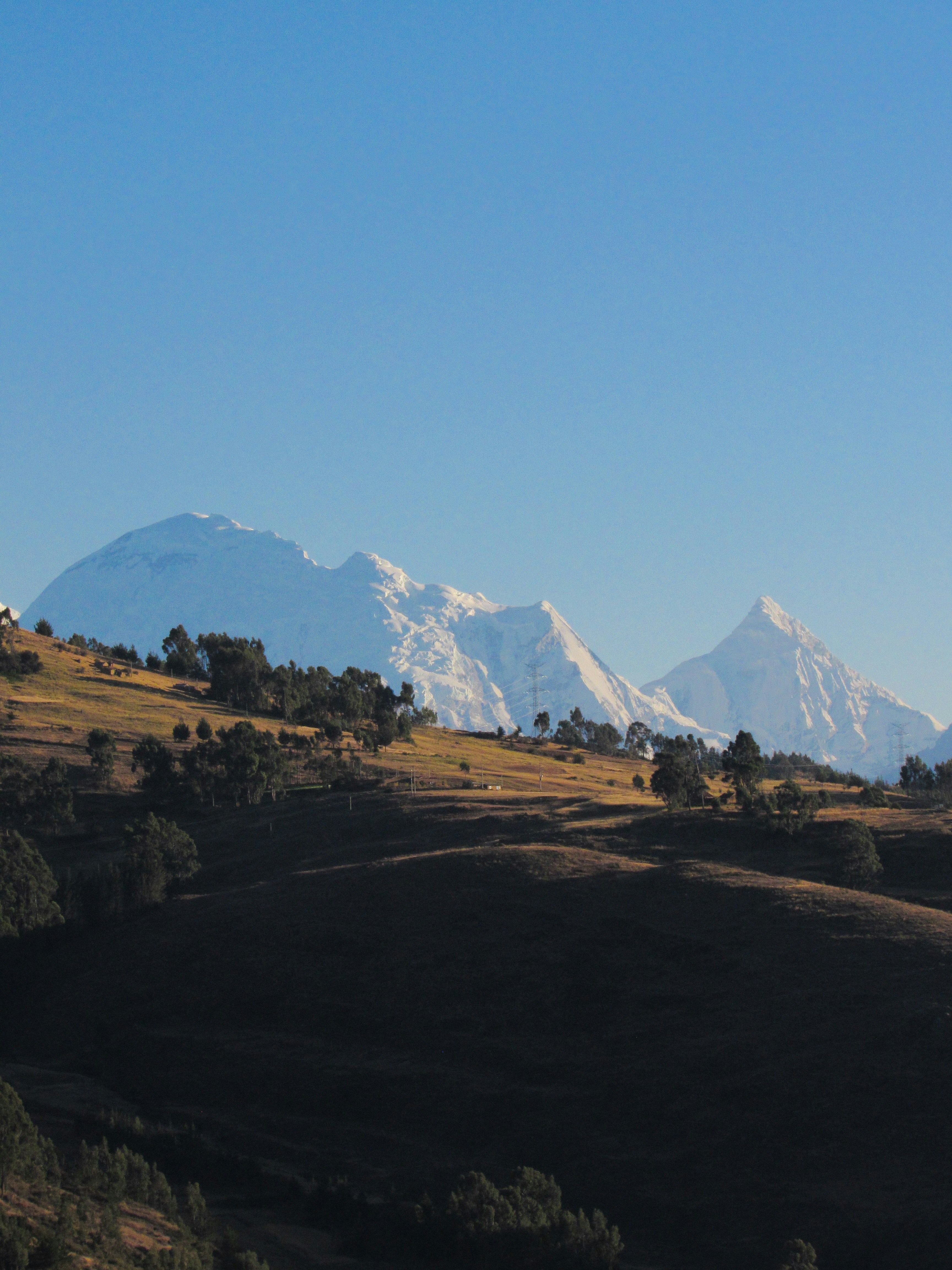 Snow-capped Andean mountains rise above sunlit rolling hills under a clear blue sky.