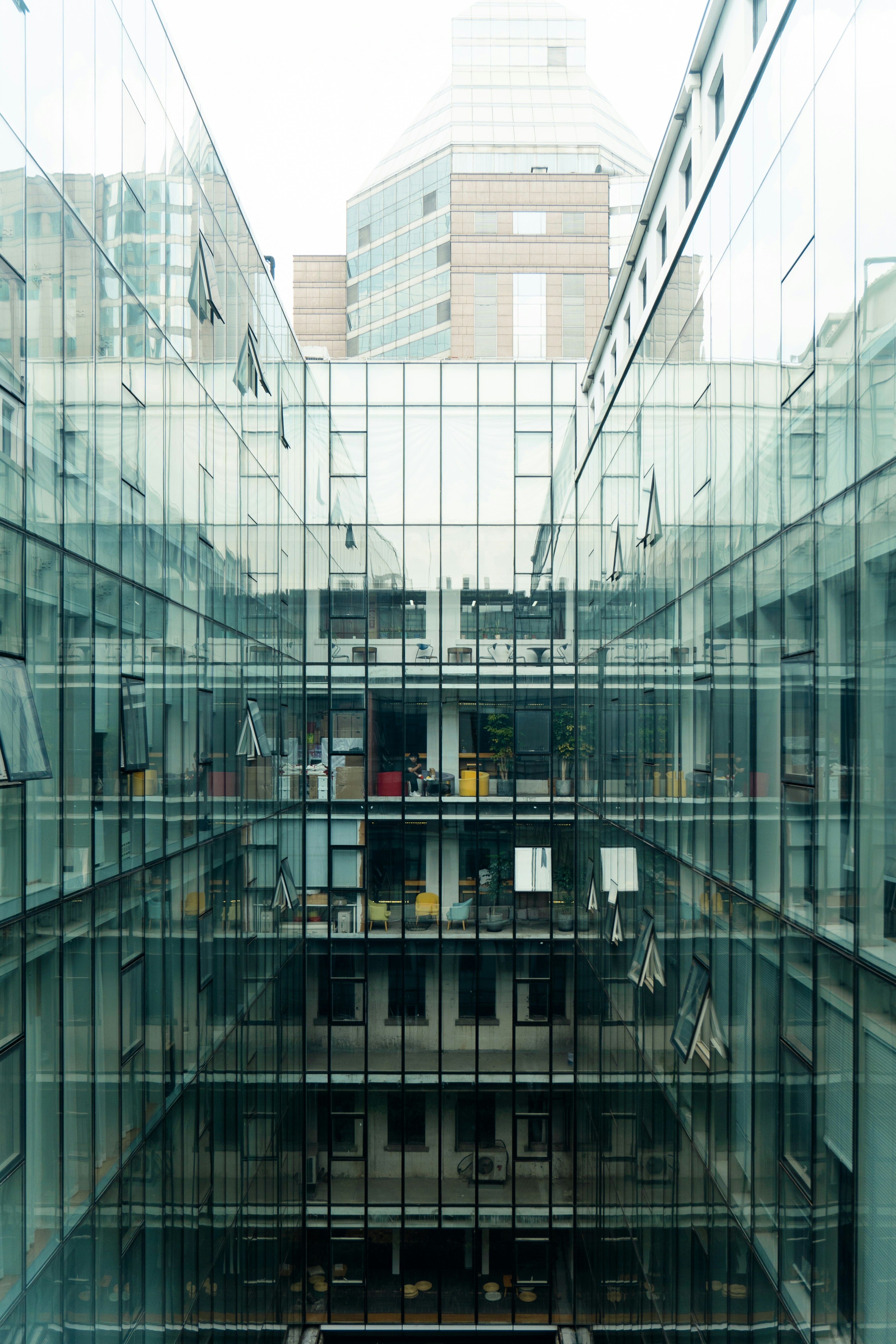 Symmetrical glass facade reflecting an inner courtyard with distant city buildings.