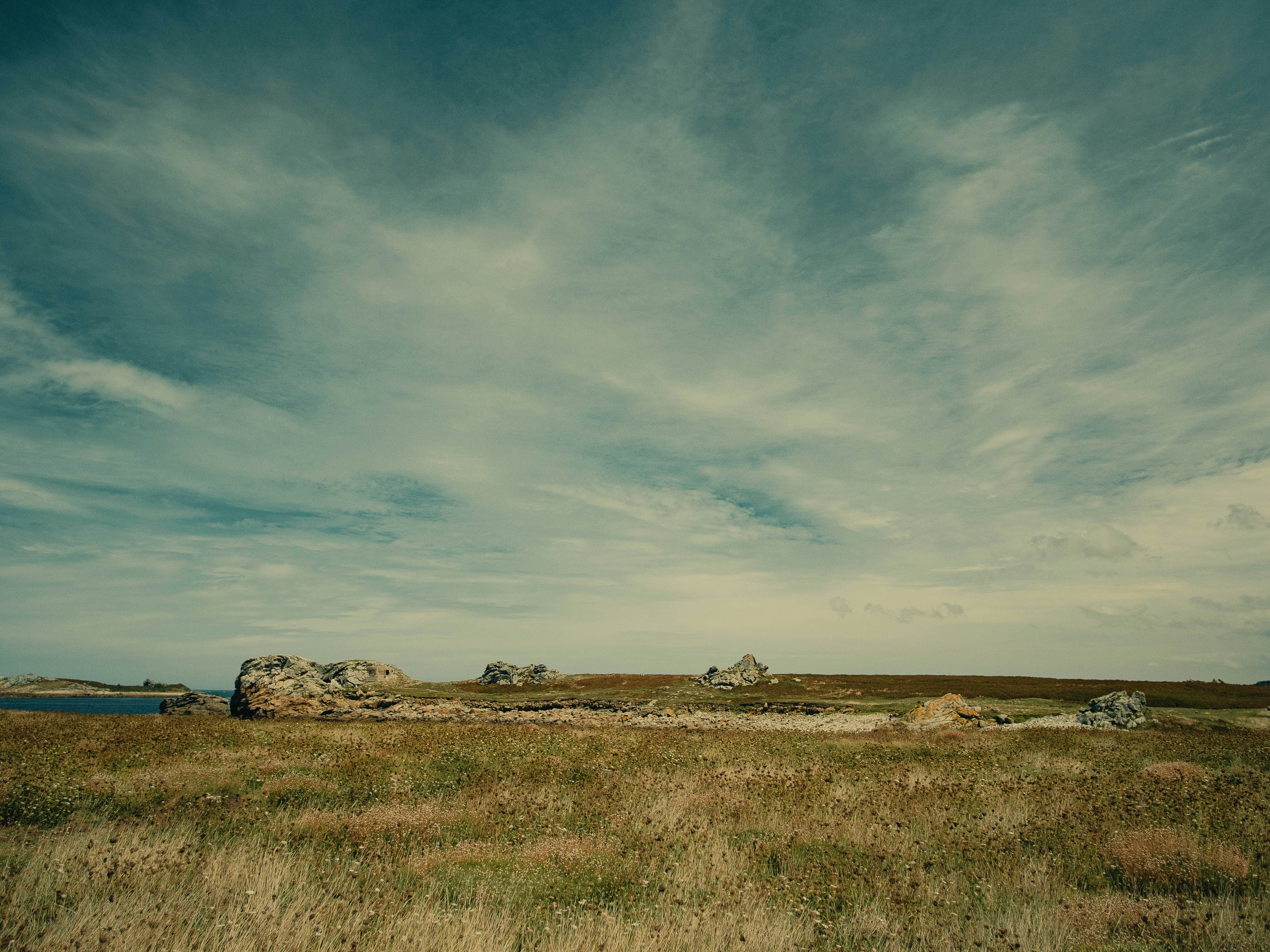 Field of rocks and grass under a vast cloudy sky with a vintage aesthetic.