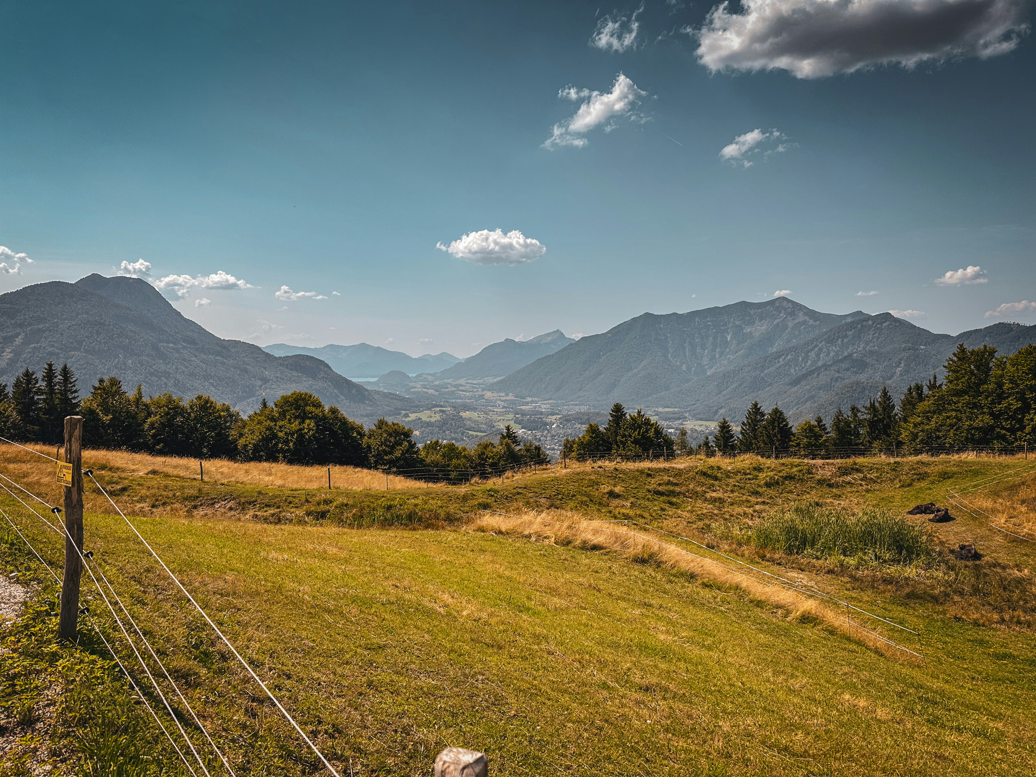 Rolling green fields with mountain ranges in the background under a clear blue sky.