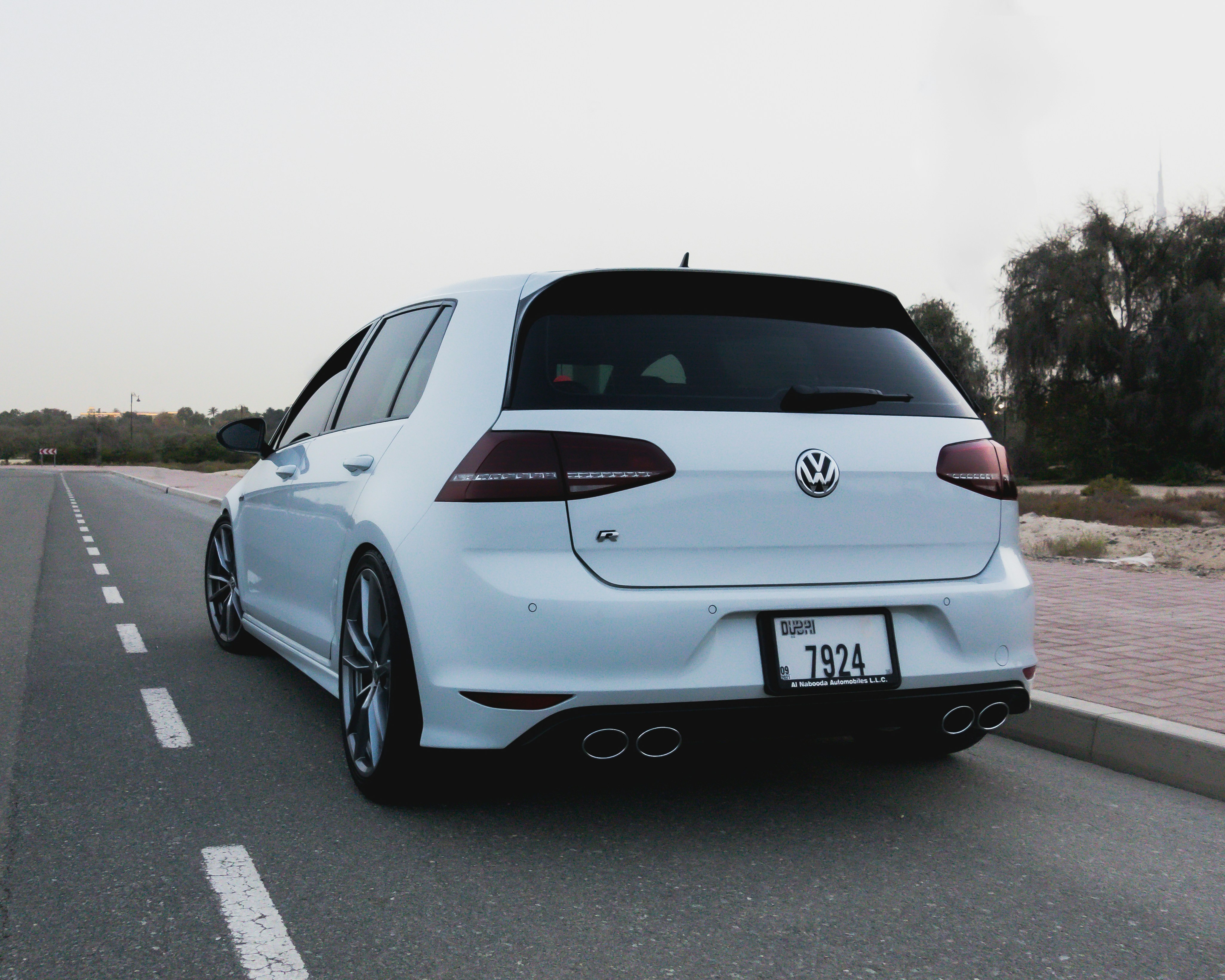 Tail lights and dual exhaust: a white VW hatchback parked on a coastal road