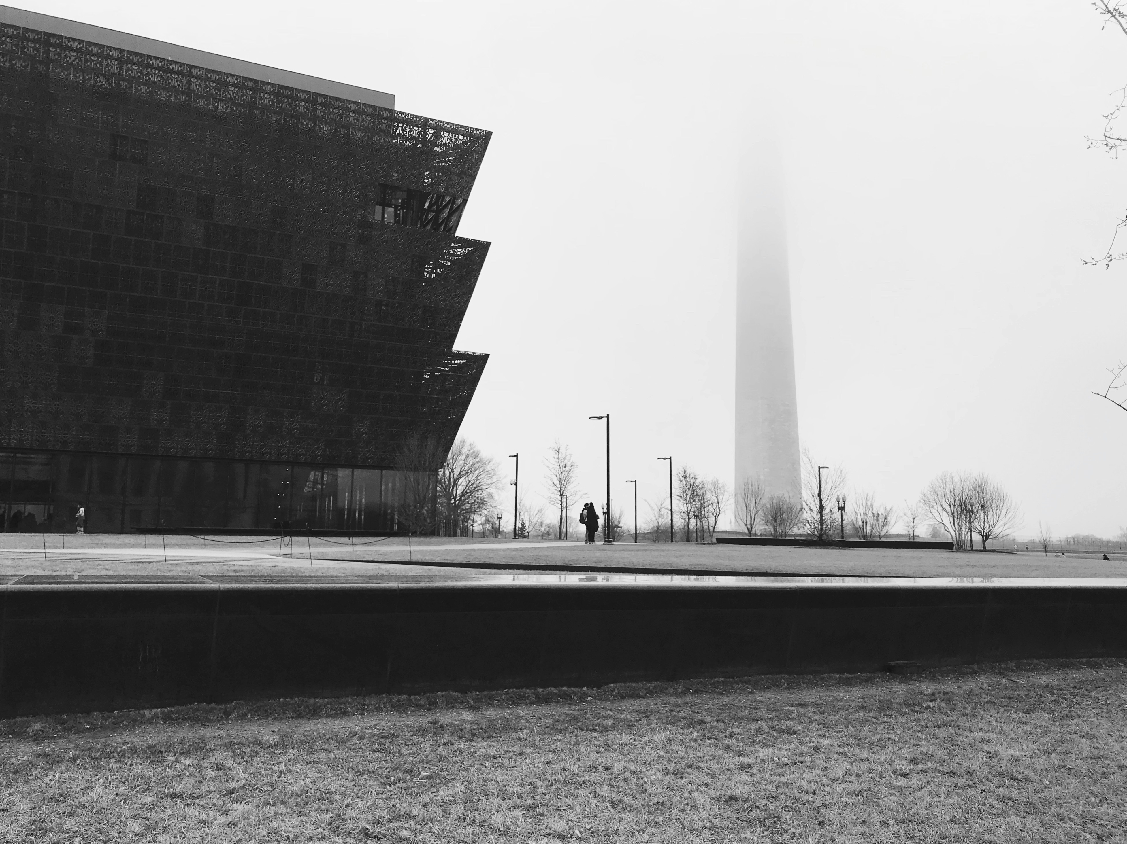 Lone Figure Between Sharp Facades and a Fog-Shrouded Monument