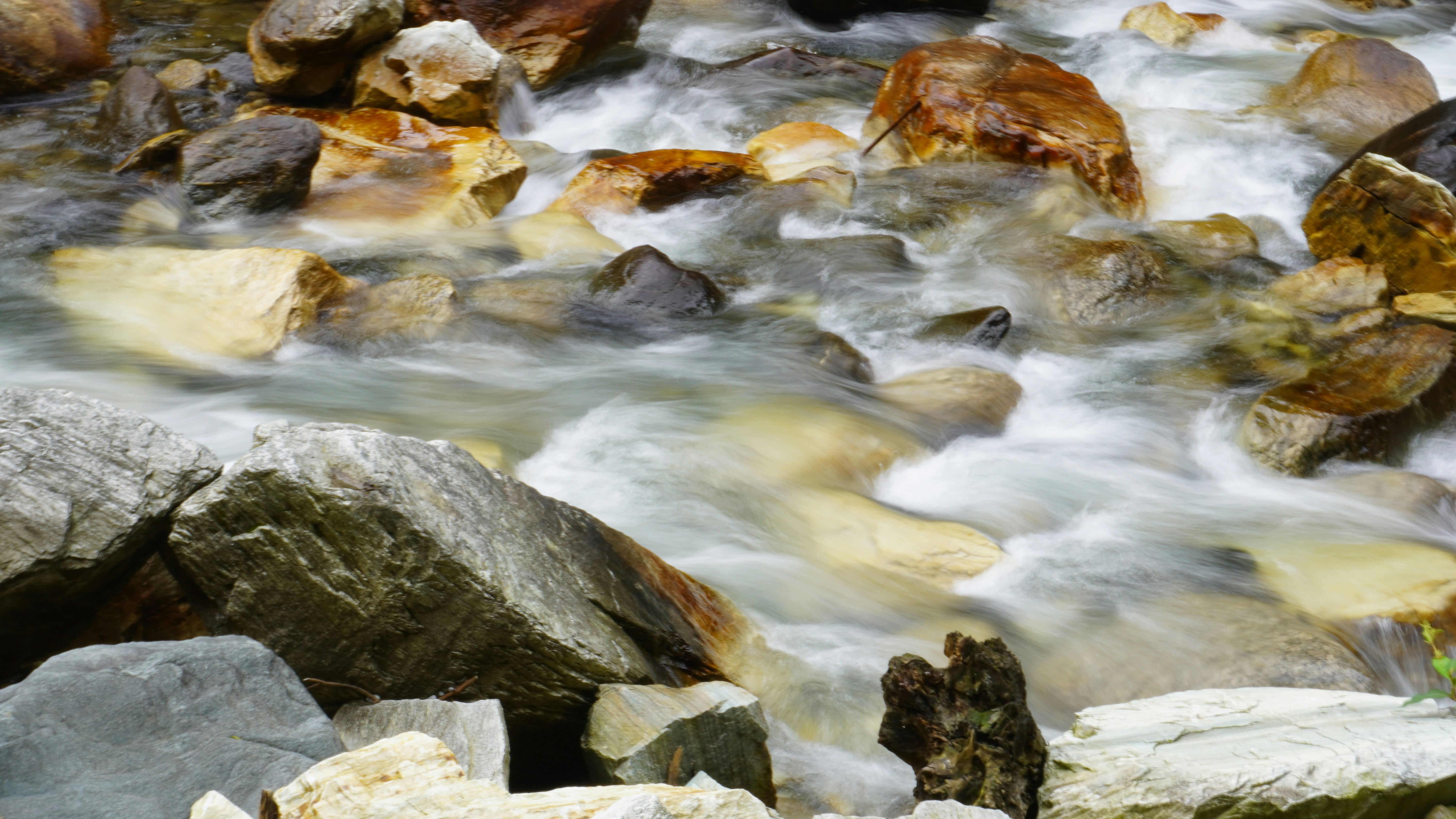 Gentle stream cascading over a bed of smooth, colorful stones, creating a serene natural scene. The water flows gracefully, highlighting the textures of the rocks.