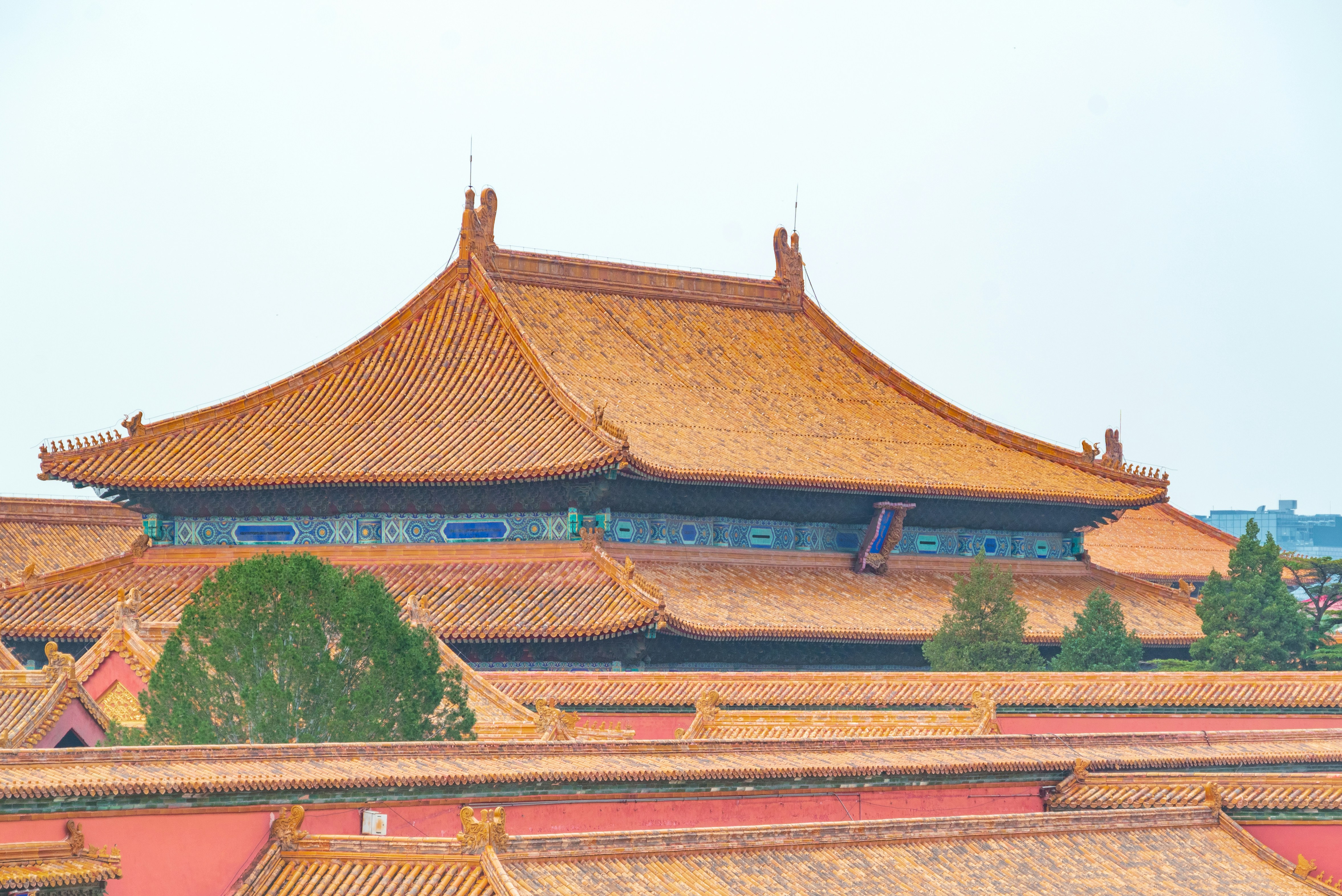 Intricate rooftops of traditional Chinese architecture showcasing vibrant orange tiles and ornate details against a pale sky.