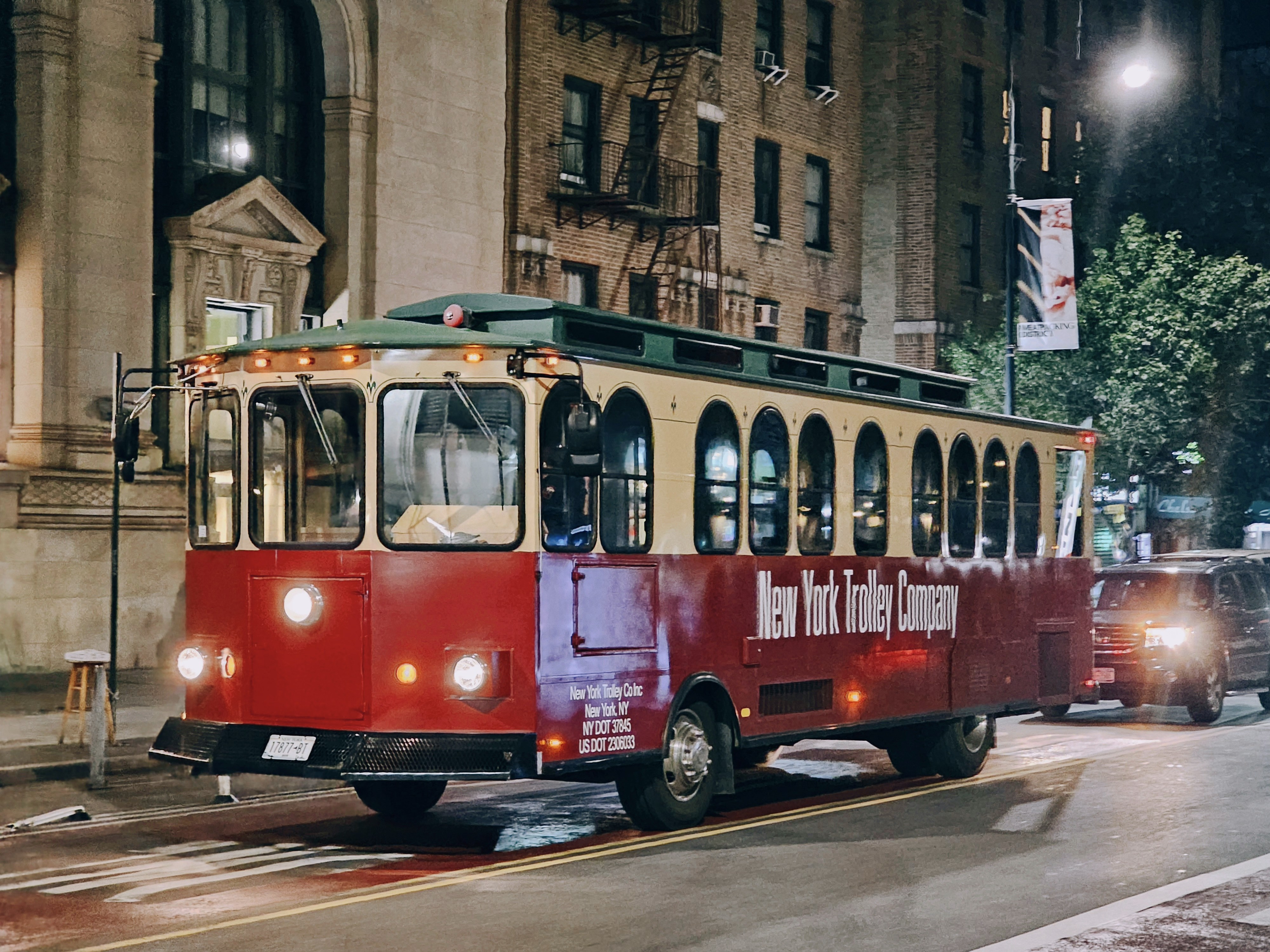Red and cream trolley driving past city buildings at night.