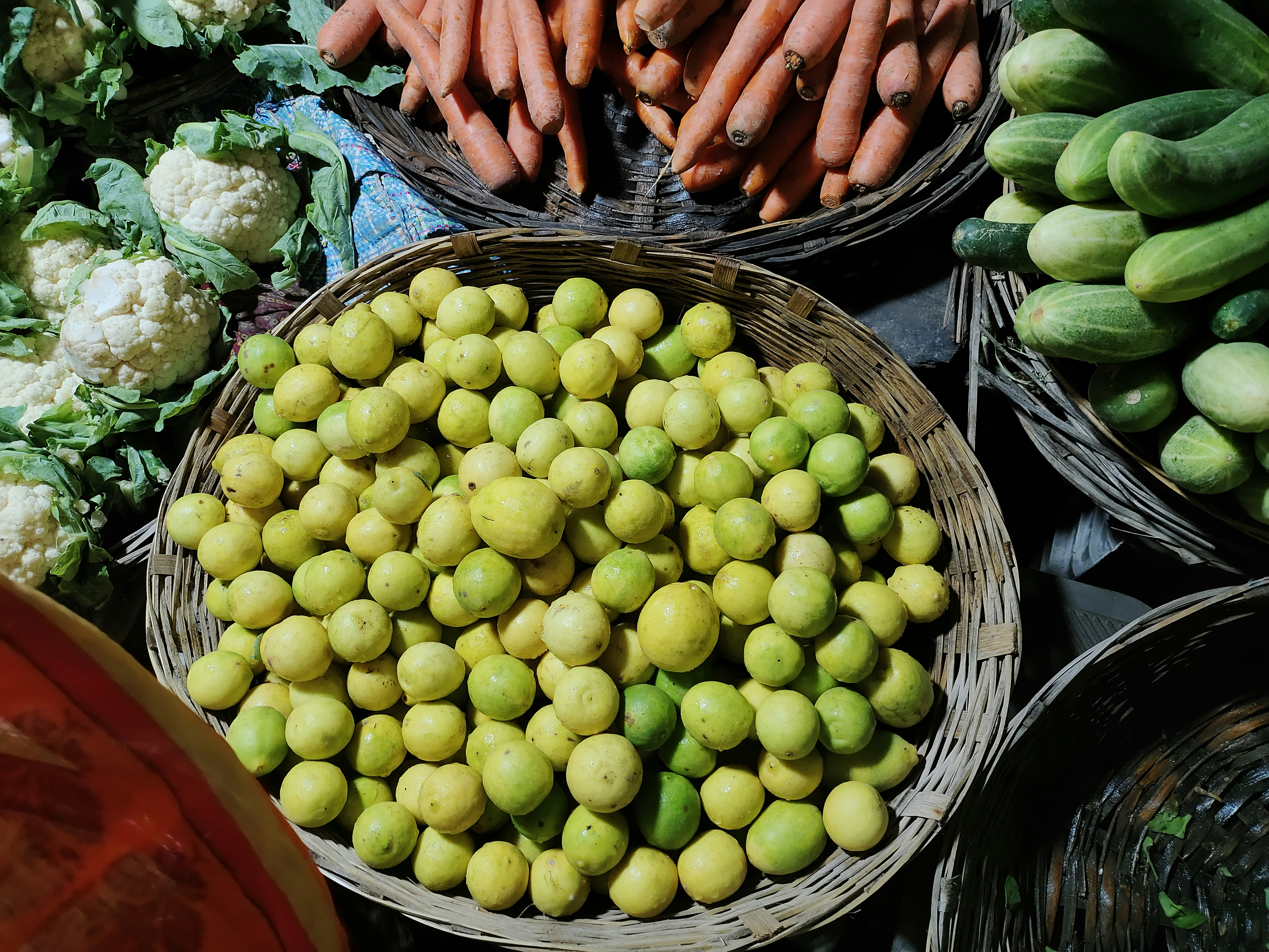 Baskets filled with lemons, carrots, and cucumbers at a street market under dim lighting.
