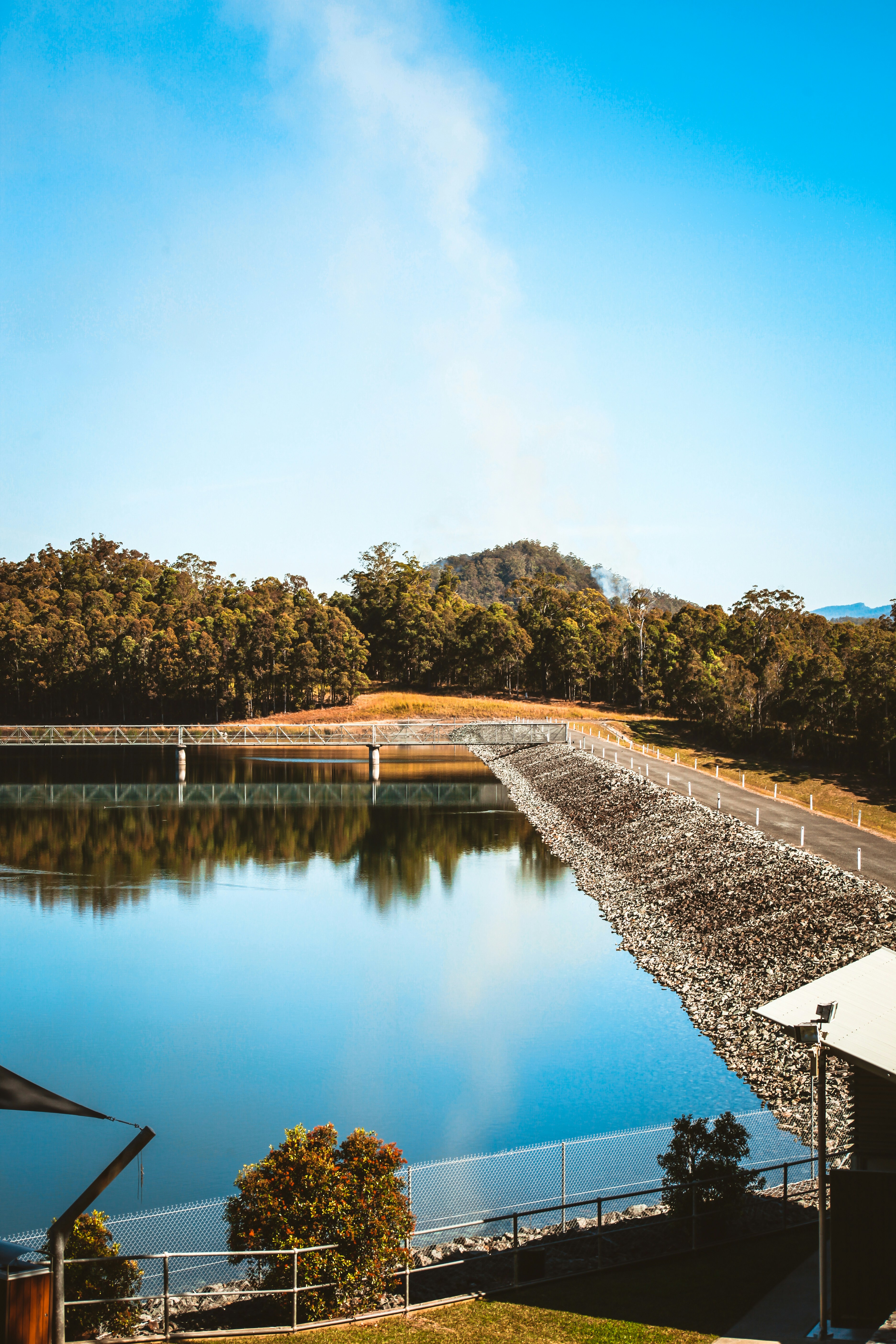 Rail-to-Reflect: A tranquil dam lined with trees and a vapor plume
