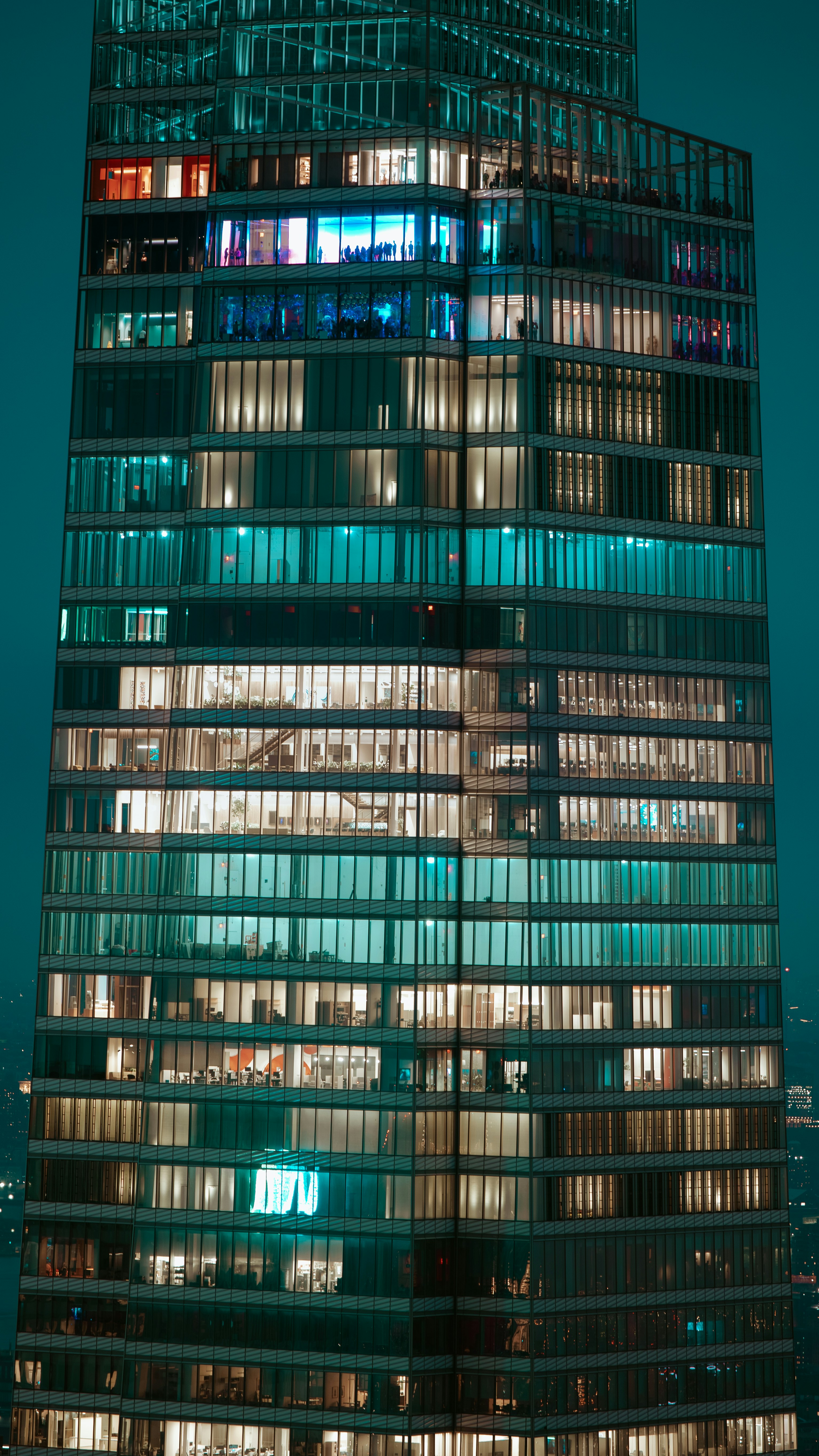 Illuminated office building showcasing vibrant reflections and silhouettes against a twilight backdrop.