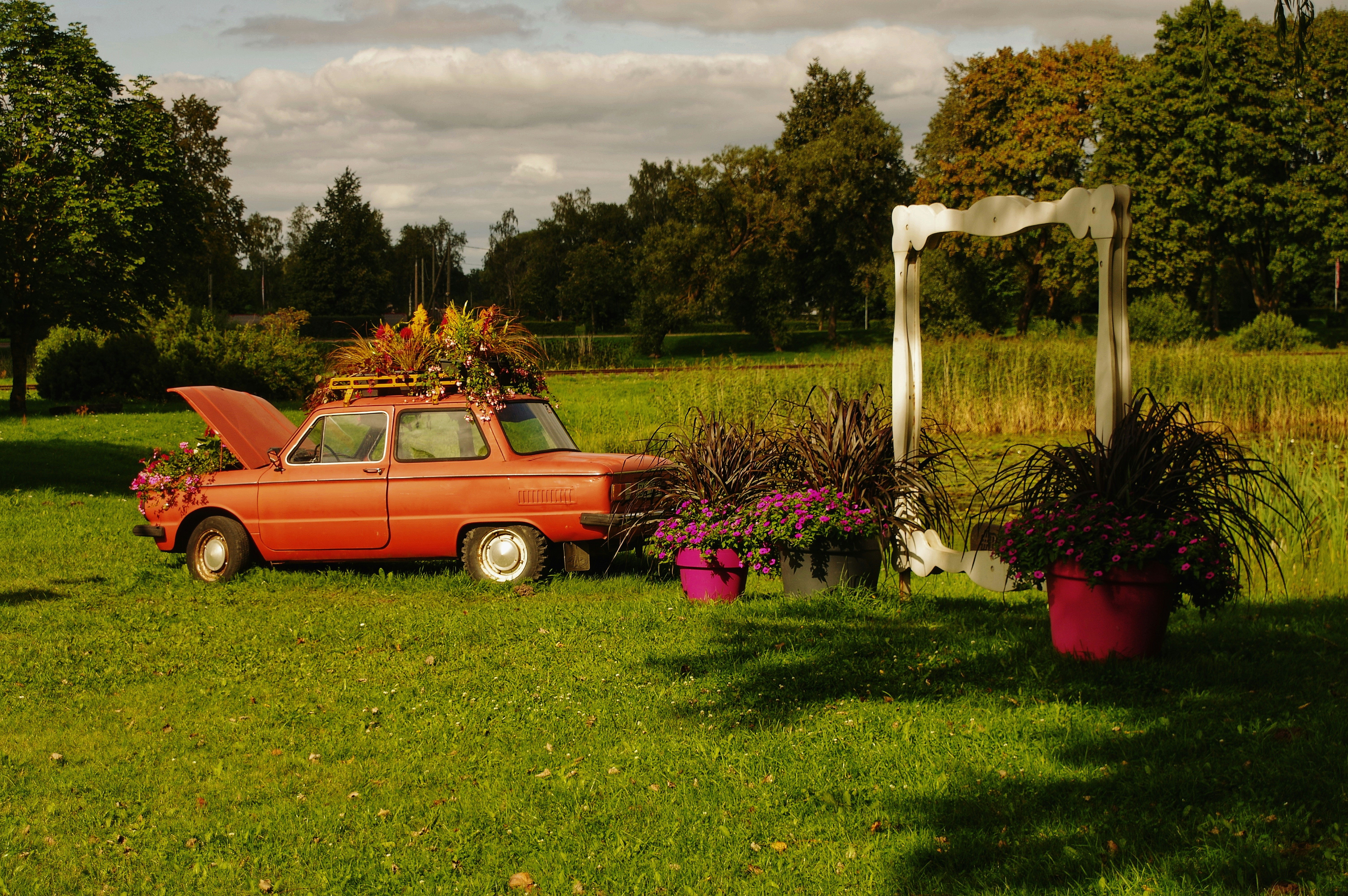 Bloom-Laden Runabout: A Vintage Orange Car Under a Floral Arch in a Sunlit Meadow