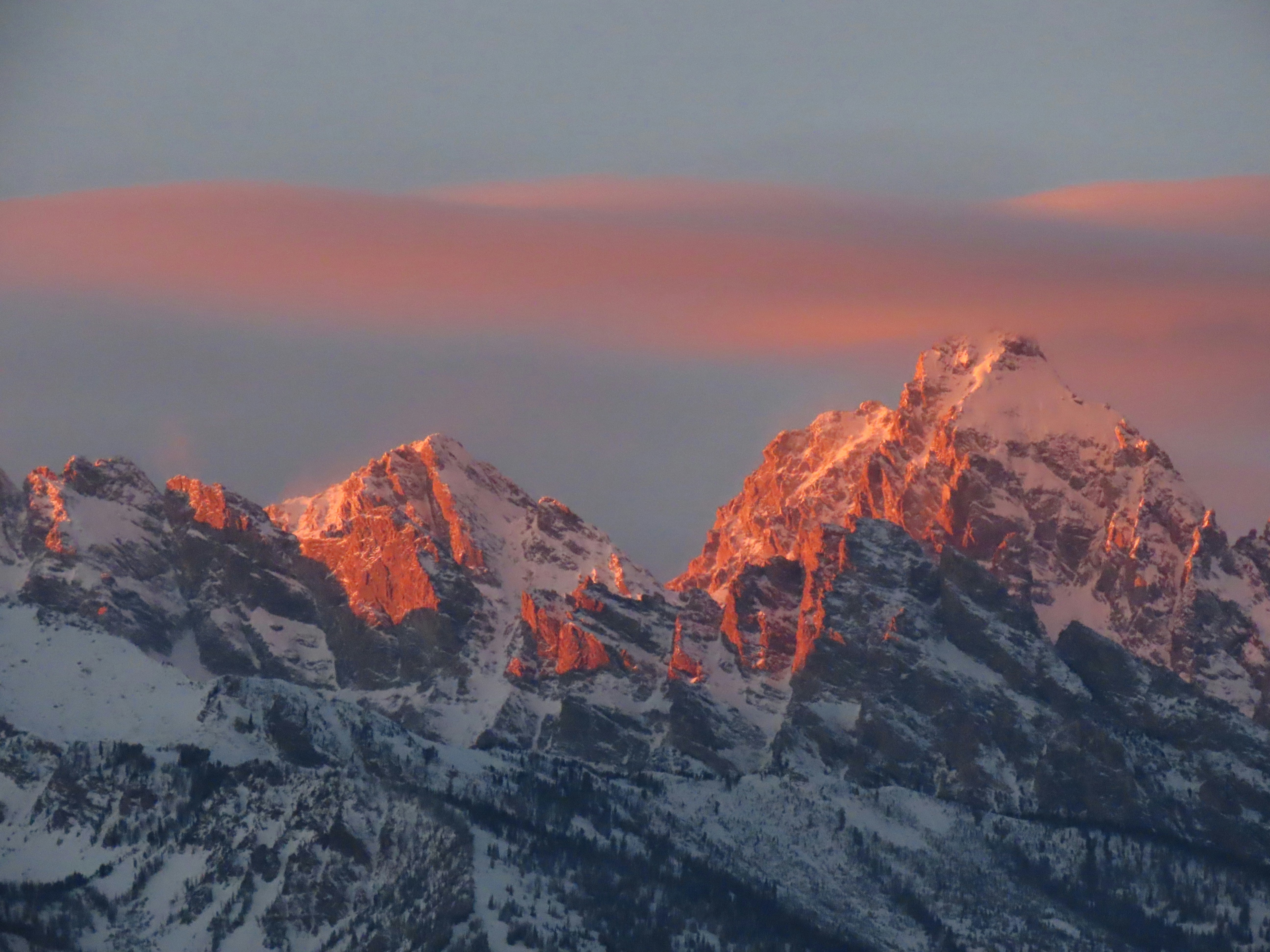 Snow-covered peaks glow with warm sunrise light along jagged ridges in a high-alpine photograph.