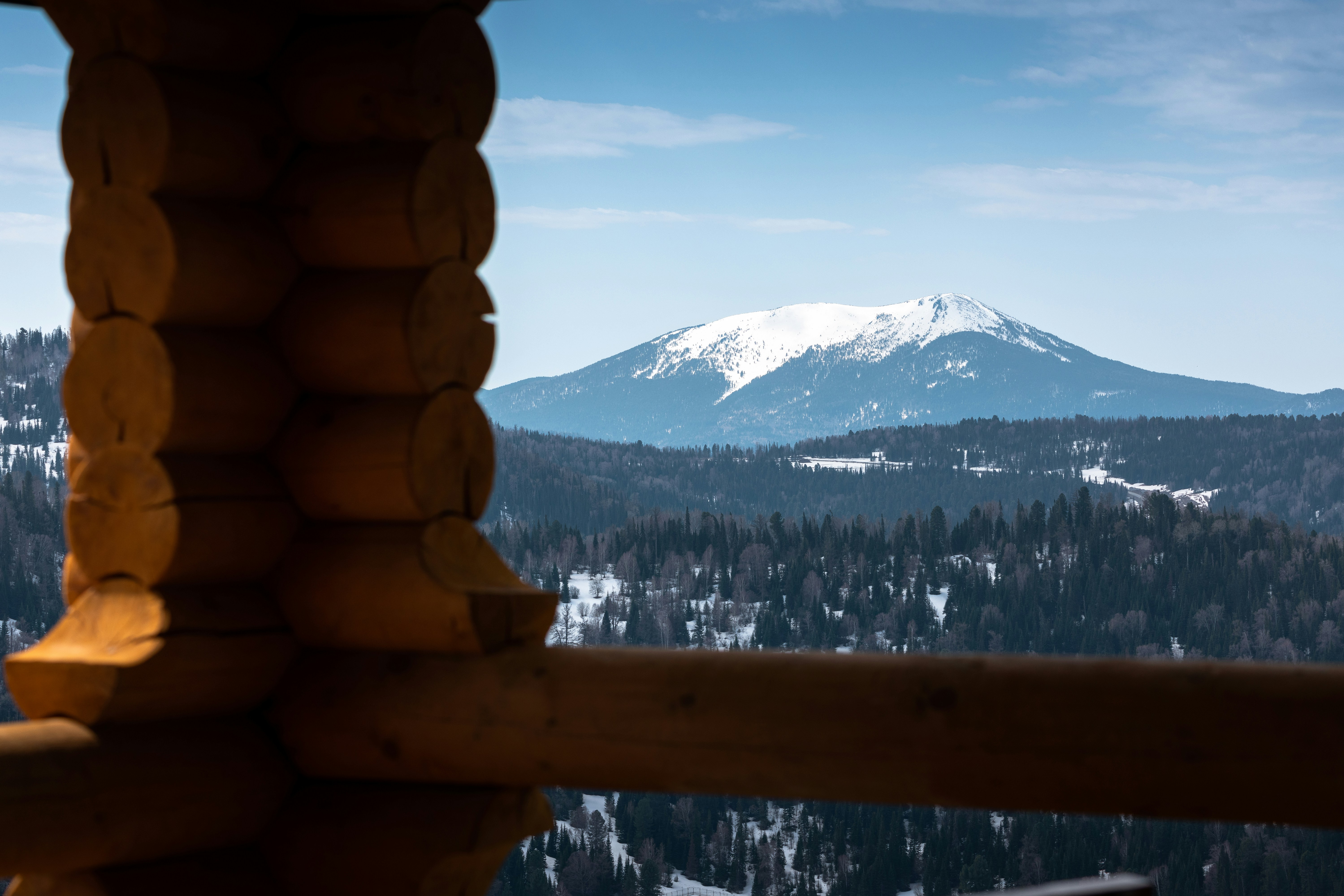 Snow-capped mountain viewed through the wooden beams of a log cabin.