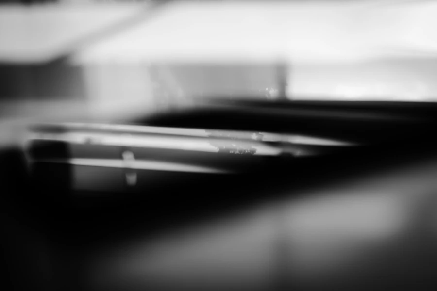 Abstract black-and-white scene with blurred reflective bands and dark shapes across a glossy surface. Light streaks and soft gradients create a minimal, out-of-focus composition.