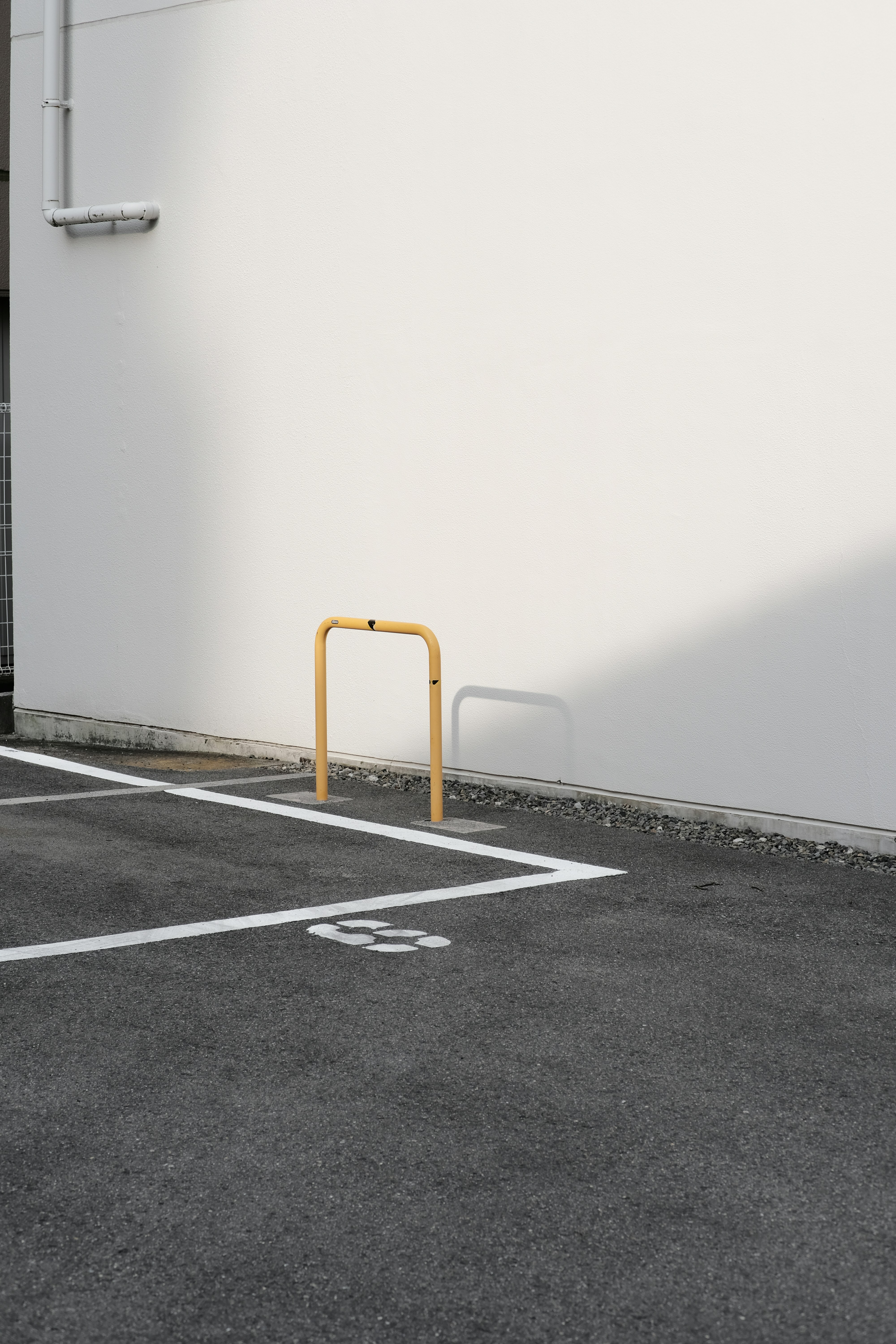 Solitary Yellow Bollard: Shadowed Geometry on a Pale Wall
