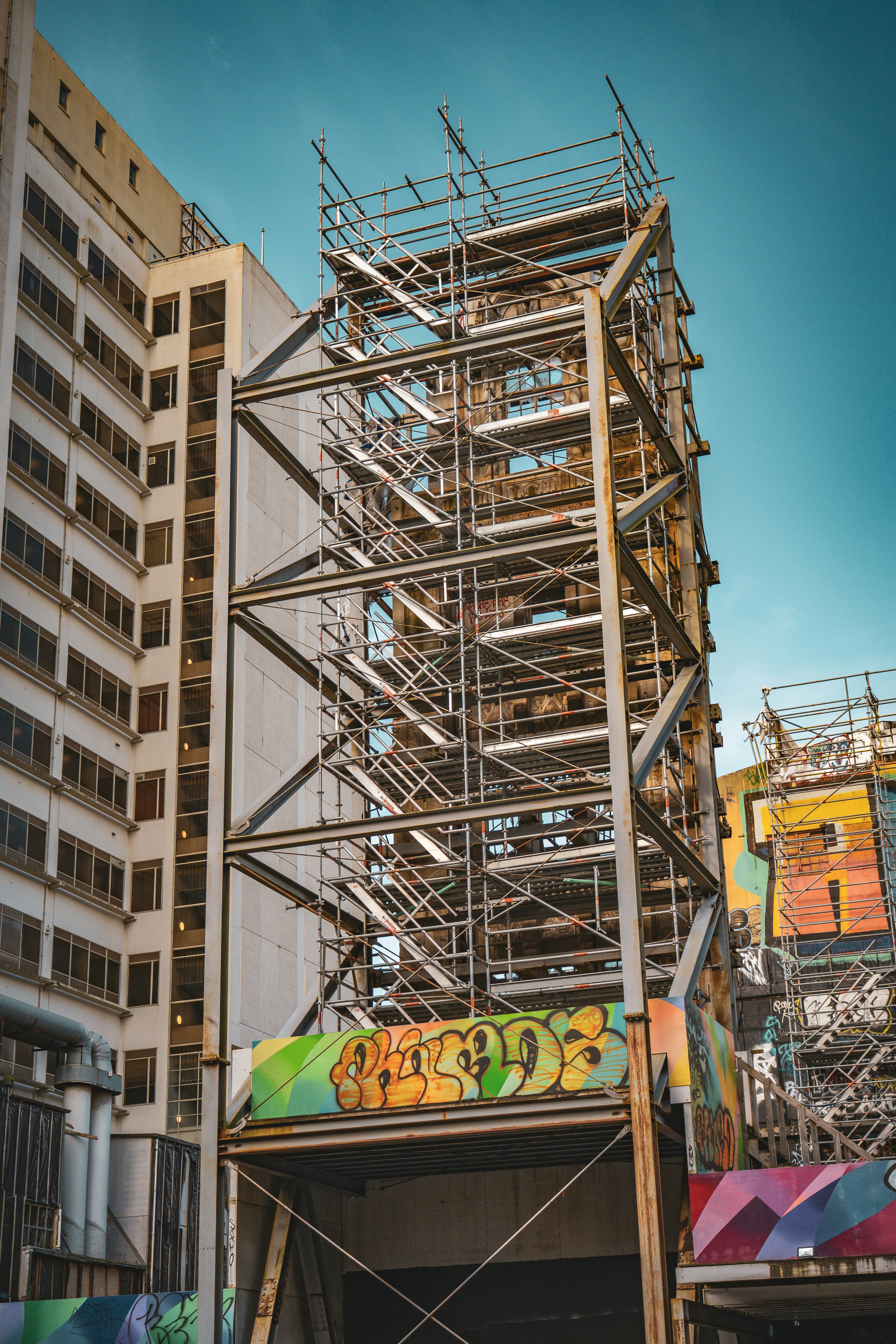 Urban Skeleton Under a Cyan Sky: Scaffold Tower Meets Graffiti