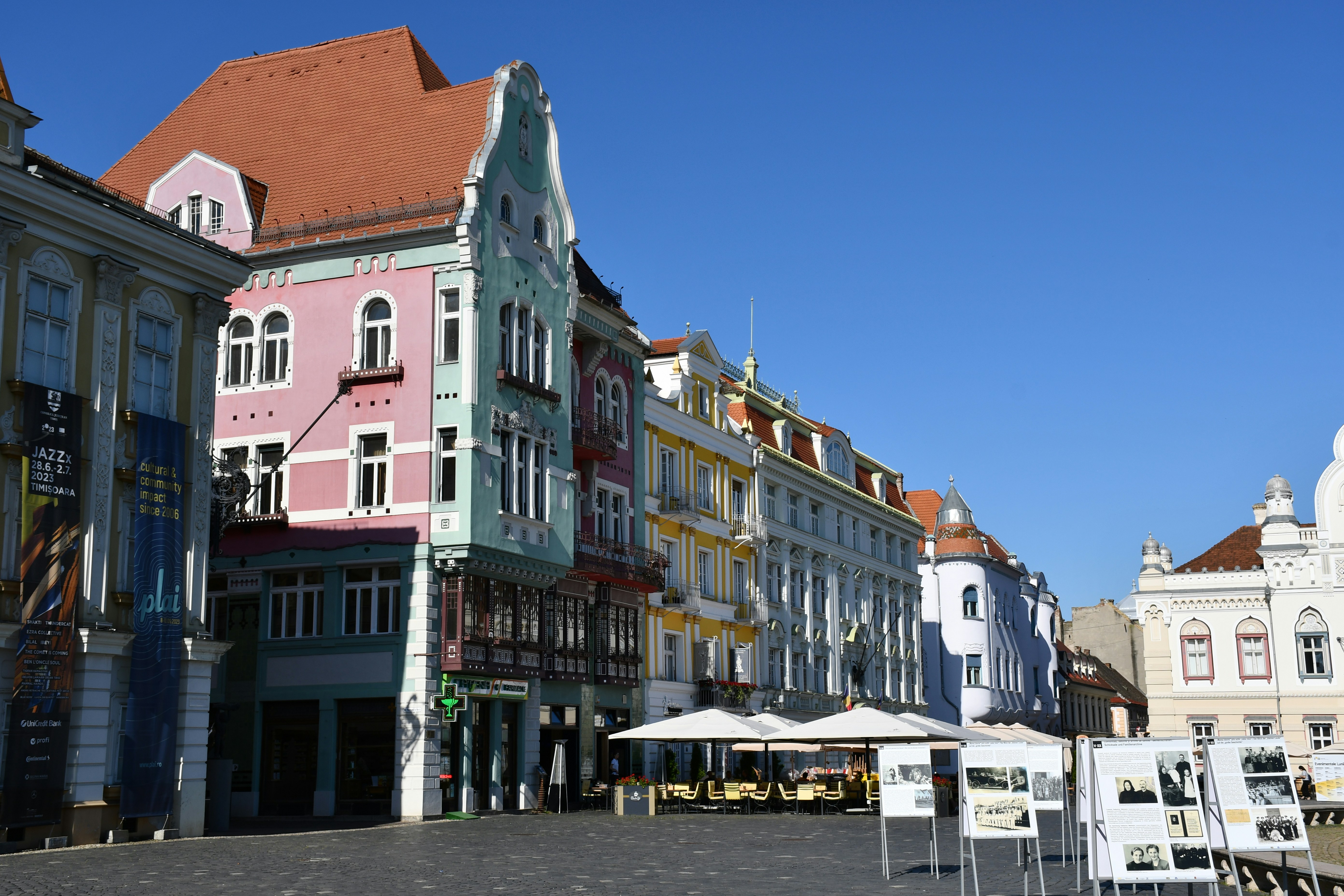 Colorful historic buildings line a sunny street in Timisoara under a clear sky.