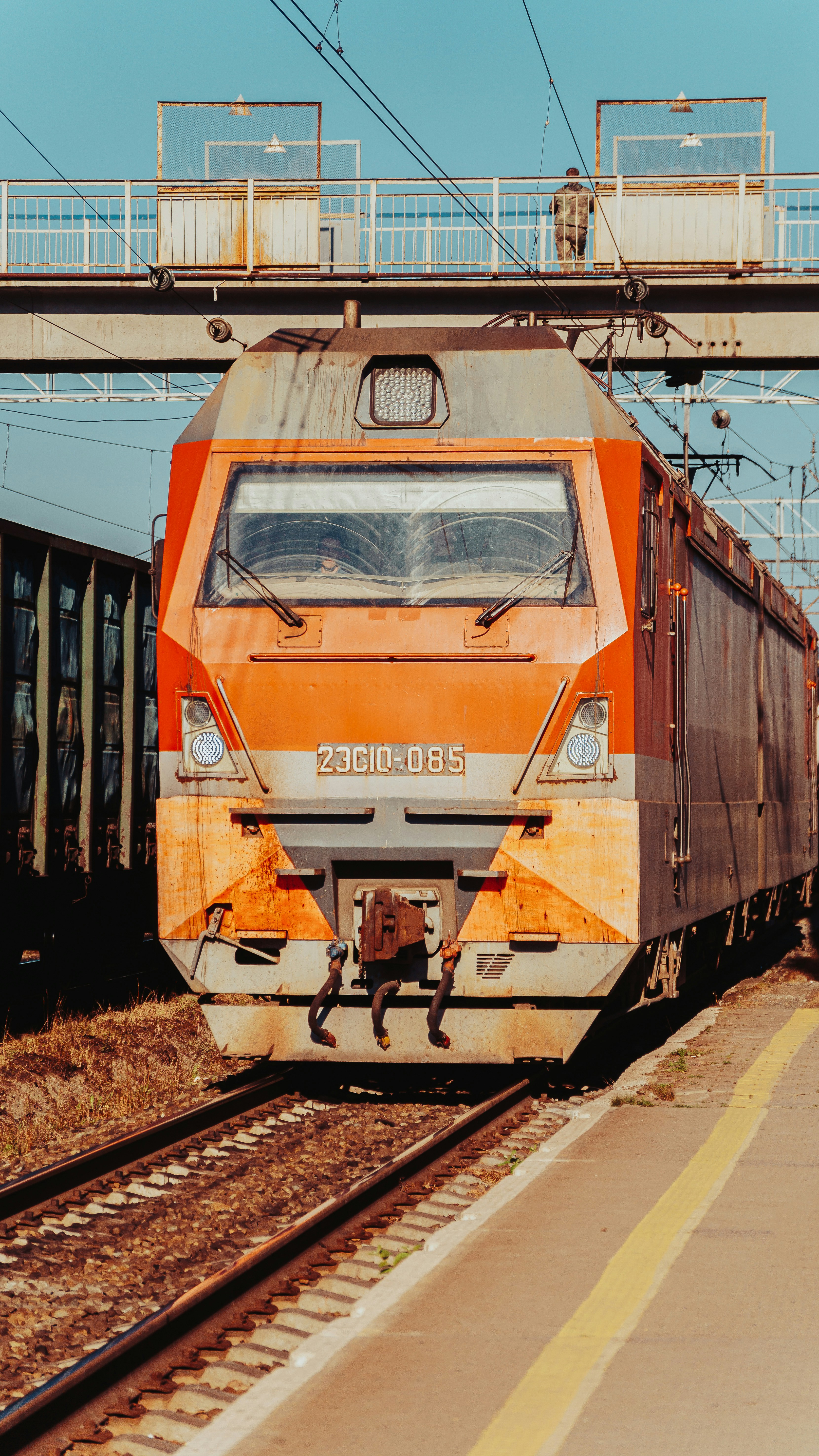 Crimson Frontline: A Weathered Locomotive Anchored by Rusted Rails and Overhead Wires
