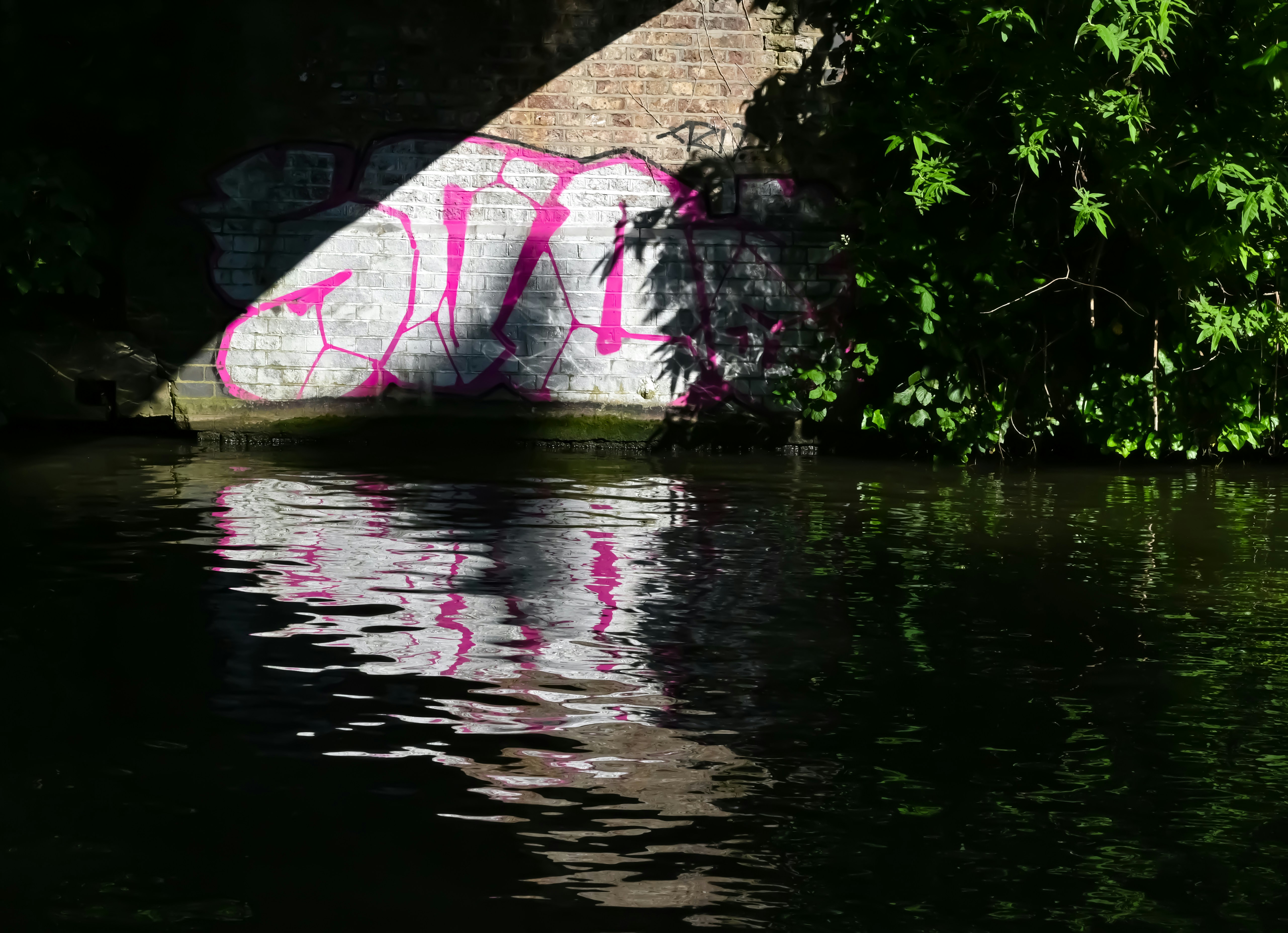 Pink Graffiti Against a Shadowed Brick Wall, Reflected in a Quiet River