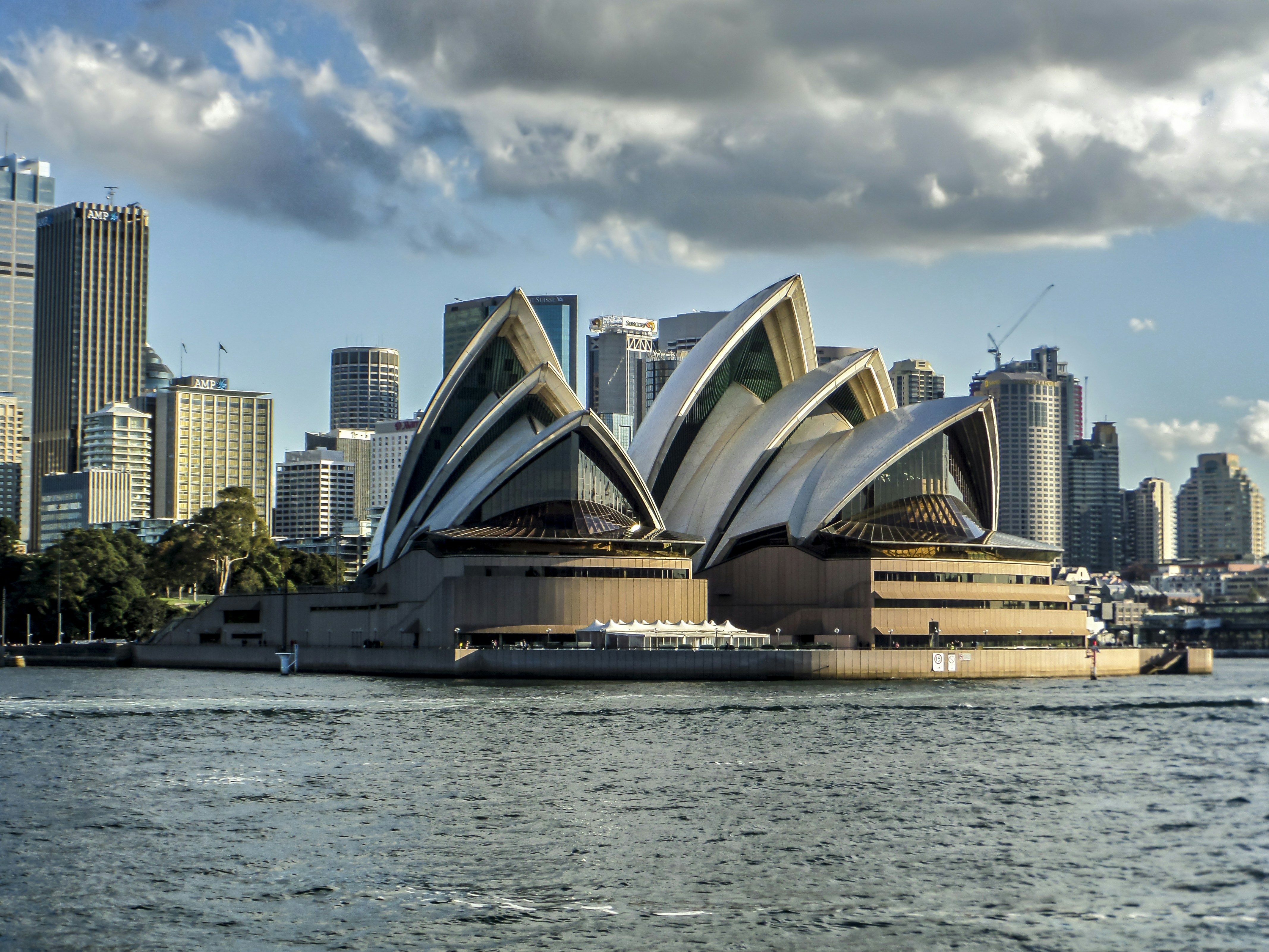 Iconic Sydney Opera House with its distinctive sail-like roof, set against a backdrop of urban skyline and water. 