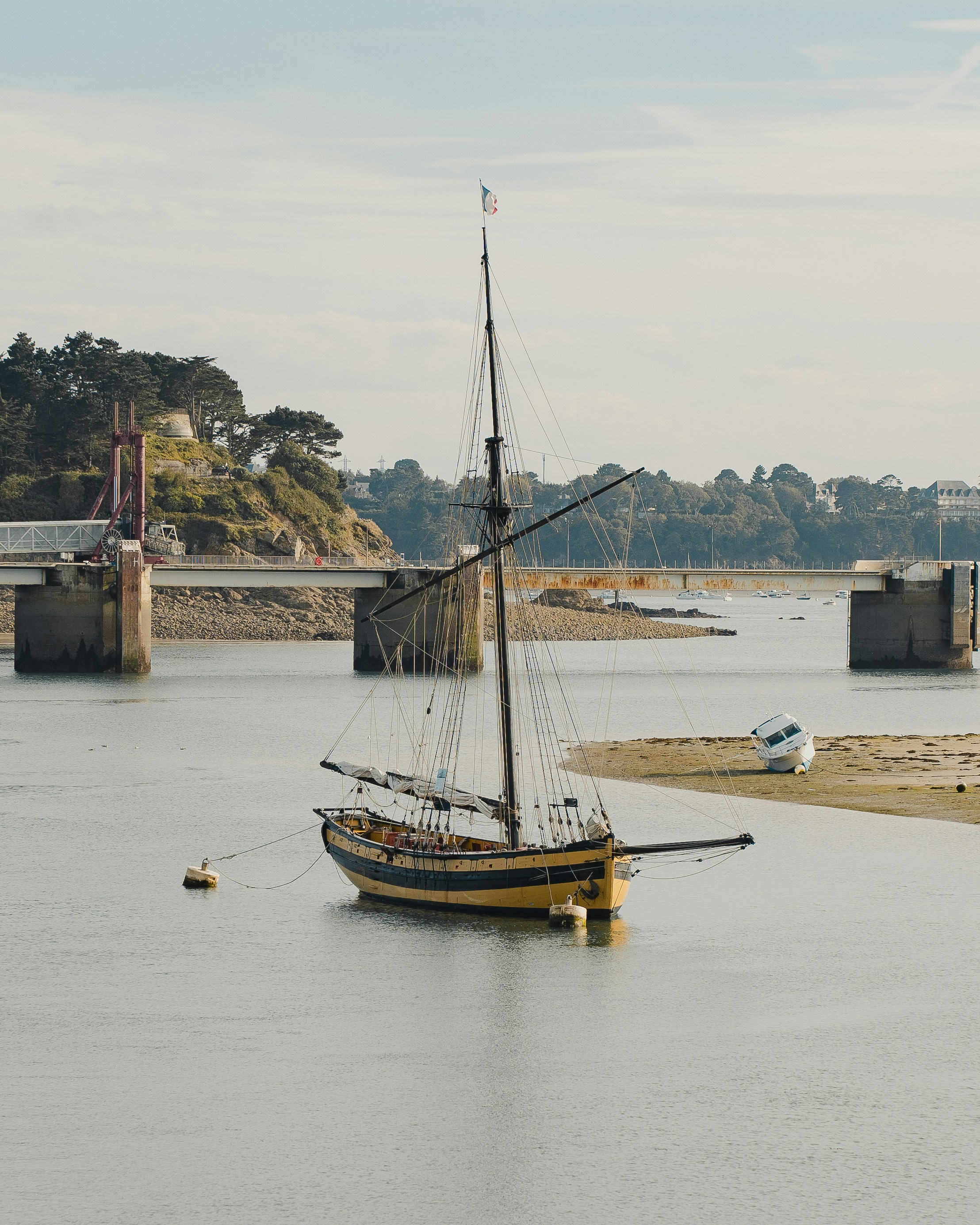 Yellow-Hulled Sailboat at Idle Tide Under a Quiet Estuary Bridge