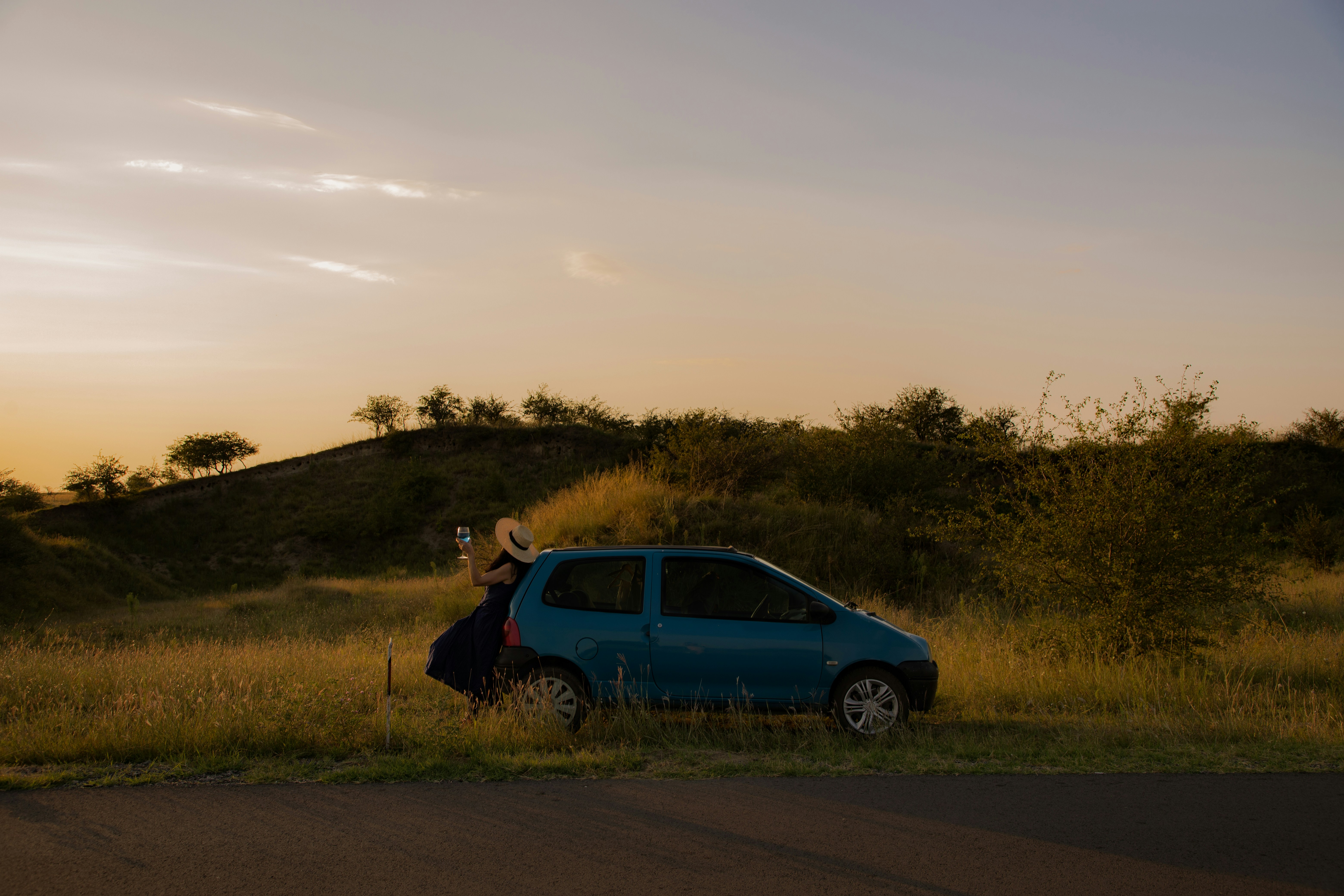 Golden Hour Standby: A Blue Hatchback and a Photographer Amid Tall Grass