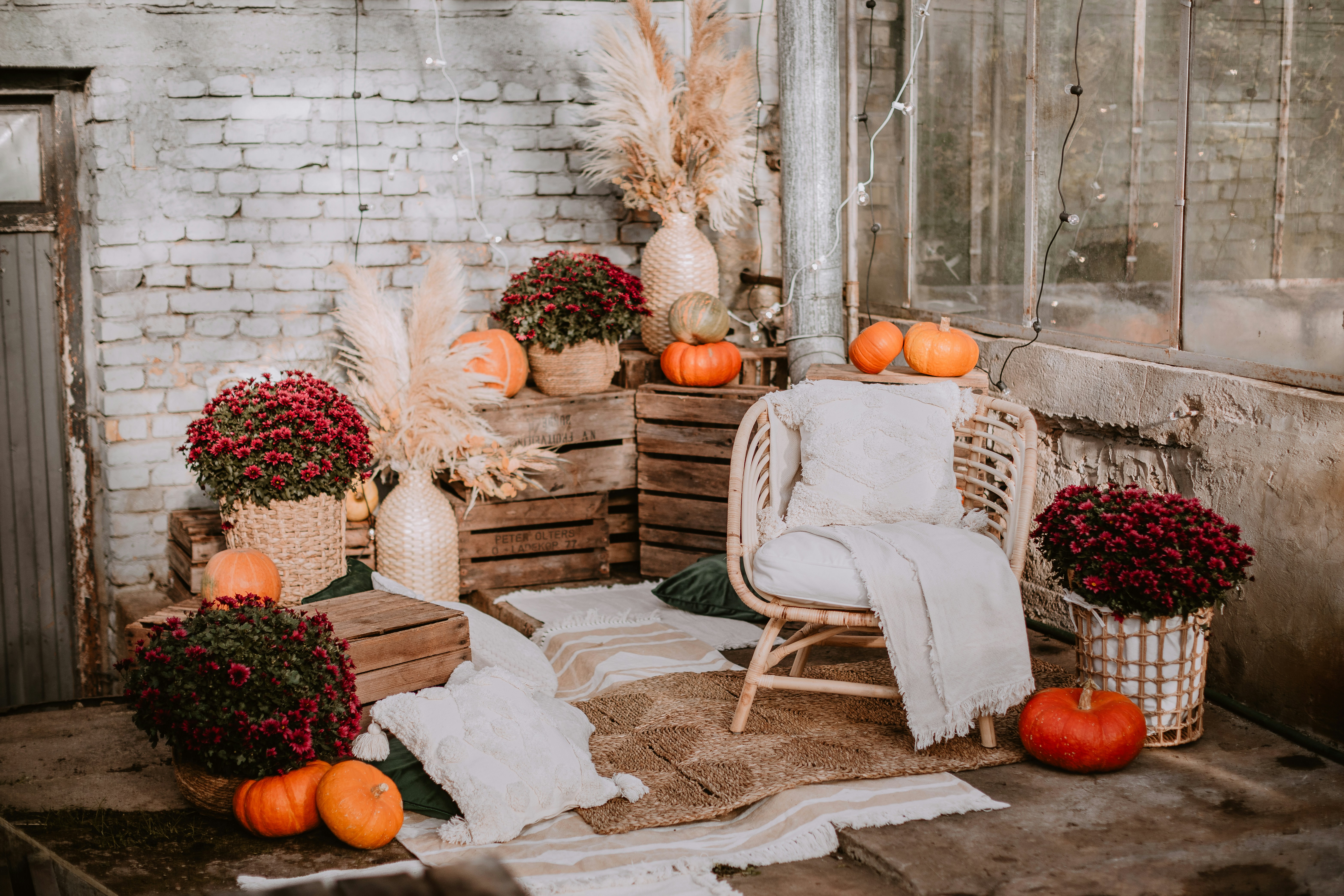 A warm autumnal scene featuring a rattan chair surrounded by pumpkins and vibrant flowers in woven baskets, set against a rustic brick wall.