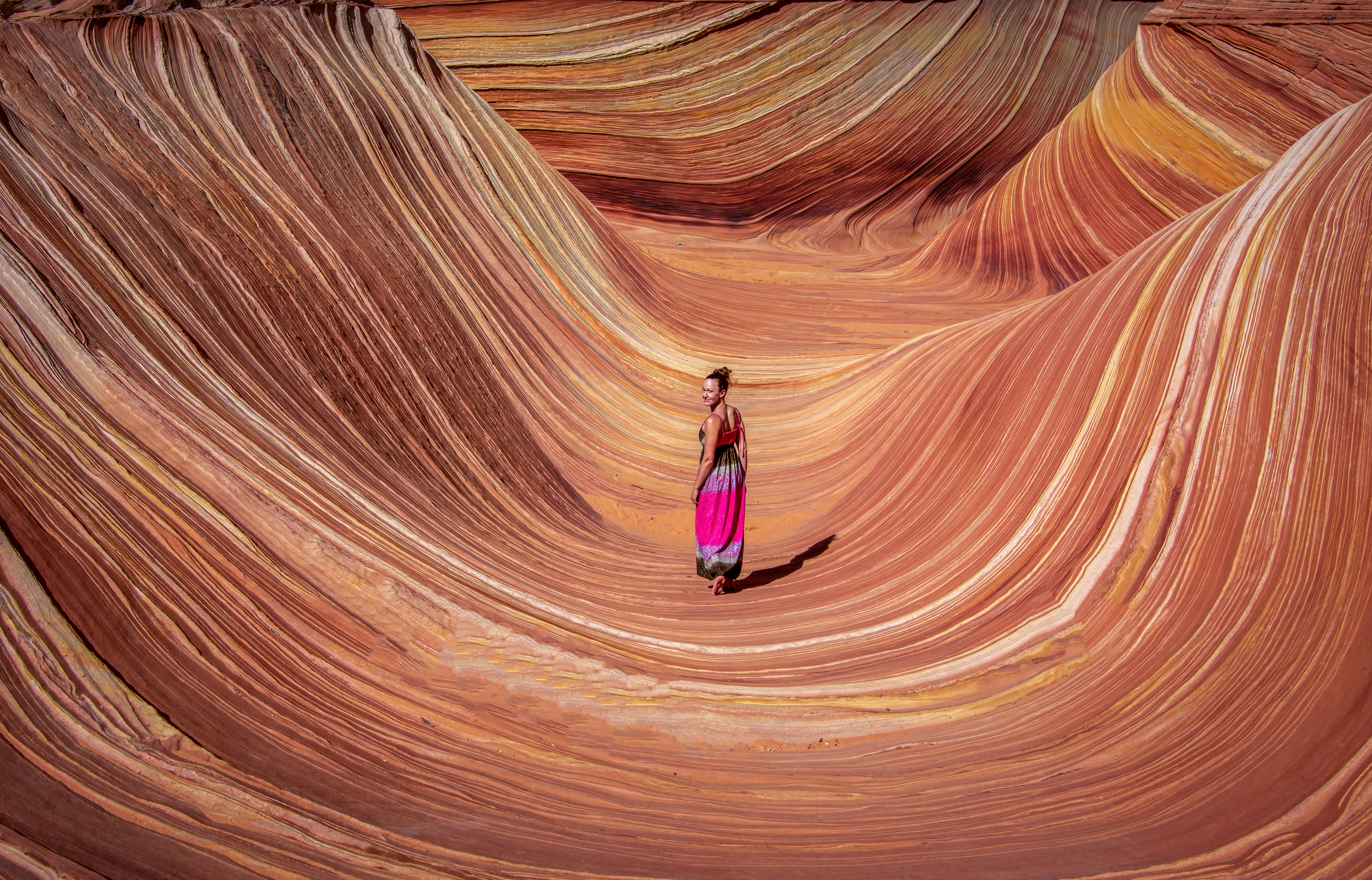 Footsteps in The Wave: A lone traveler in pink amid striped sandstone ribbons