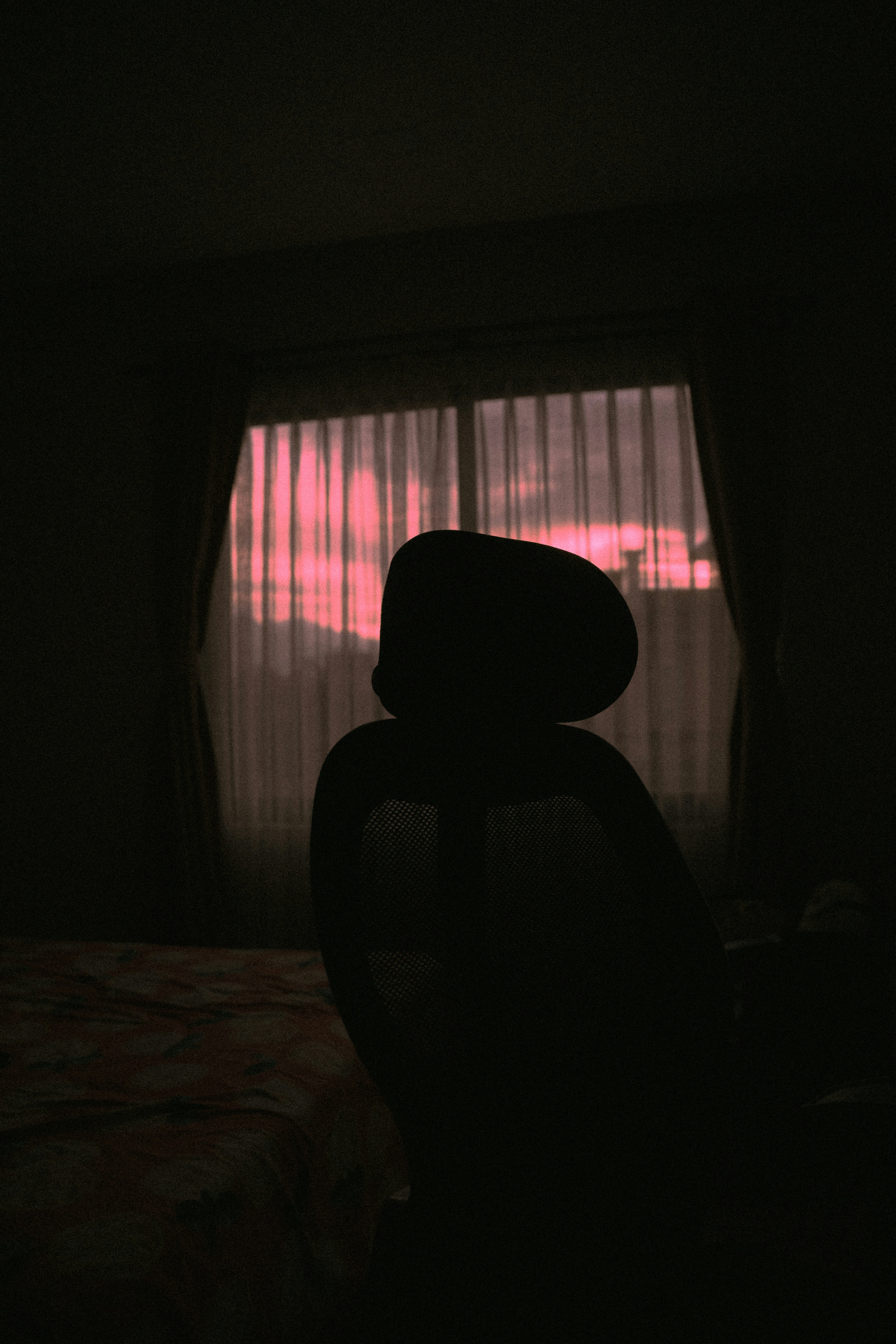 Silhouette of an office chair against a backdrop of soft pink clouds filtering through sheer curtains. The scene evokes a sense of quiet contemplation.