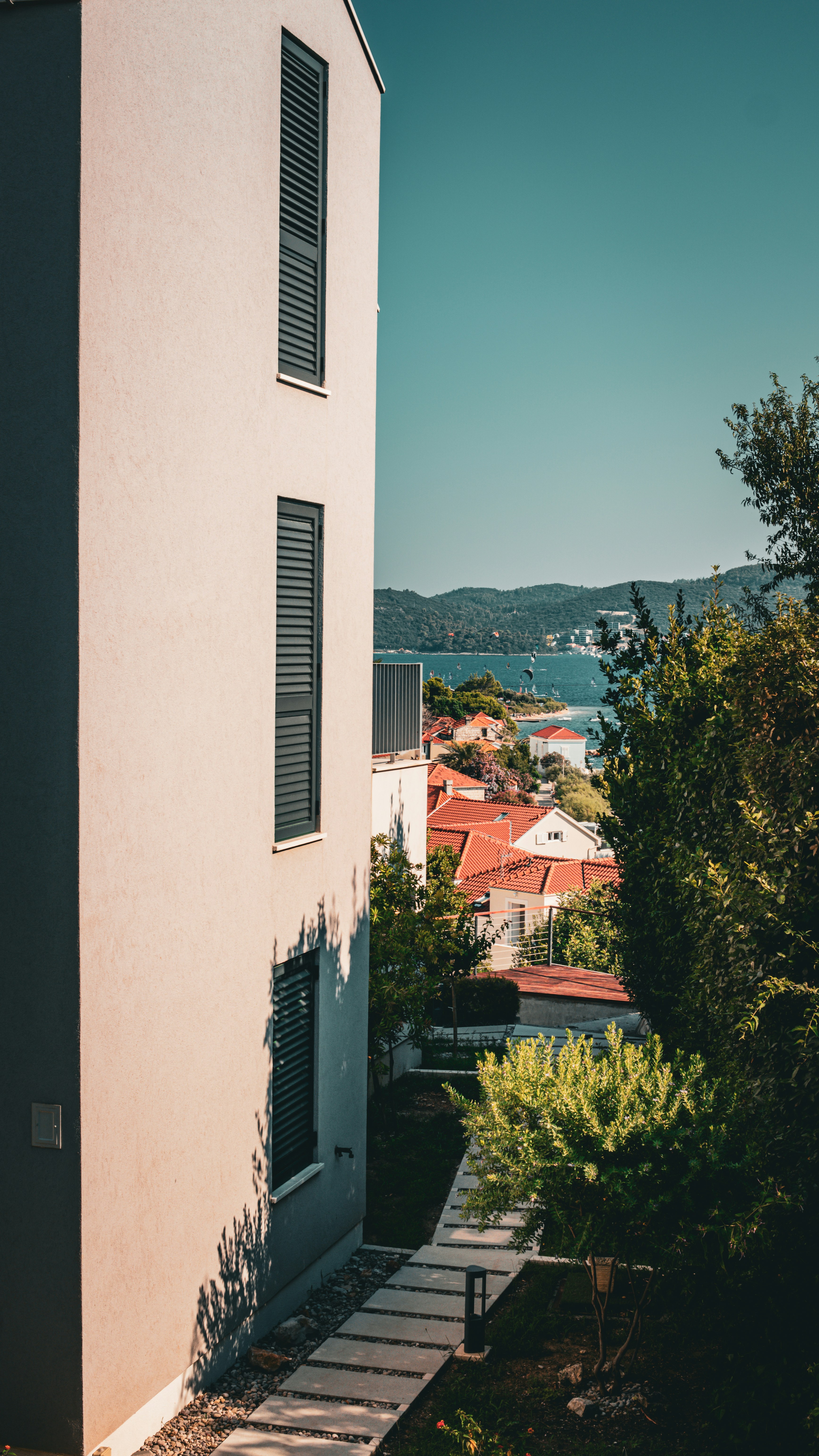Contemporary building framed by lush greenery, overlooking a tranquil coastal landscape. A pathway leads through the vibrant scenery.