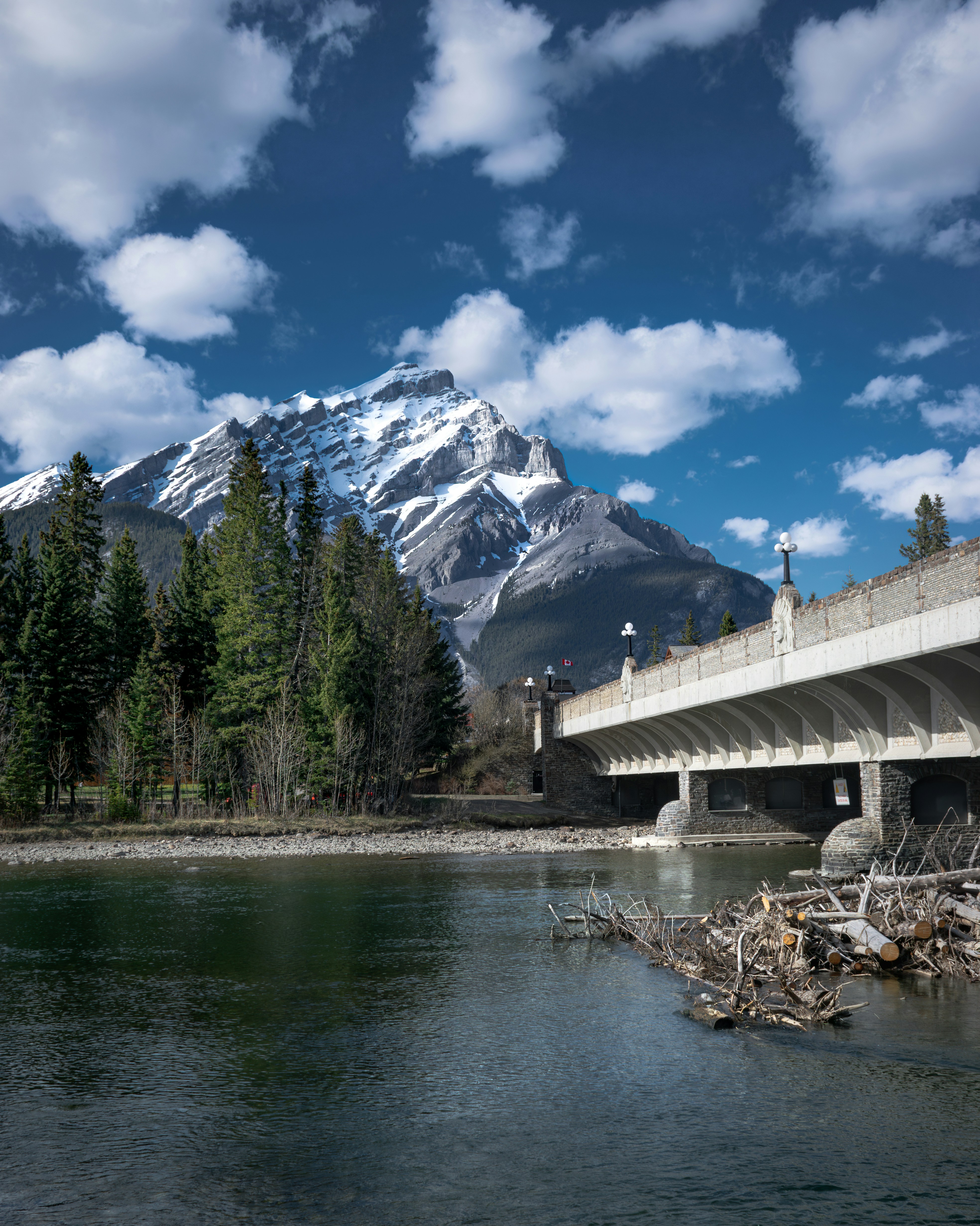 Snow-Crowned Peak Framed by Pines and a Riverside Bridge