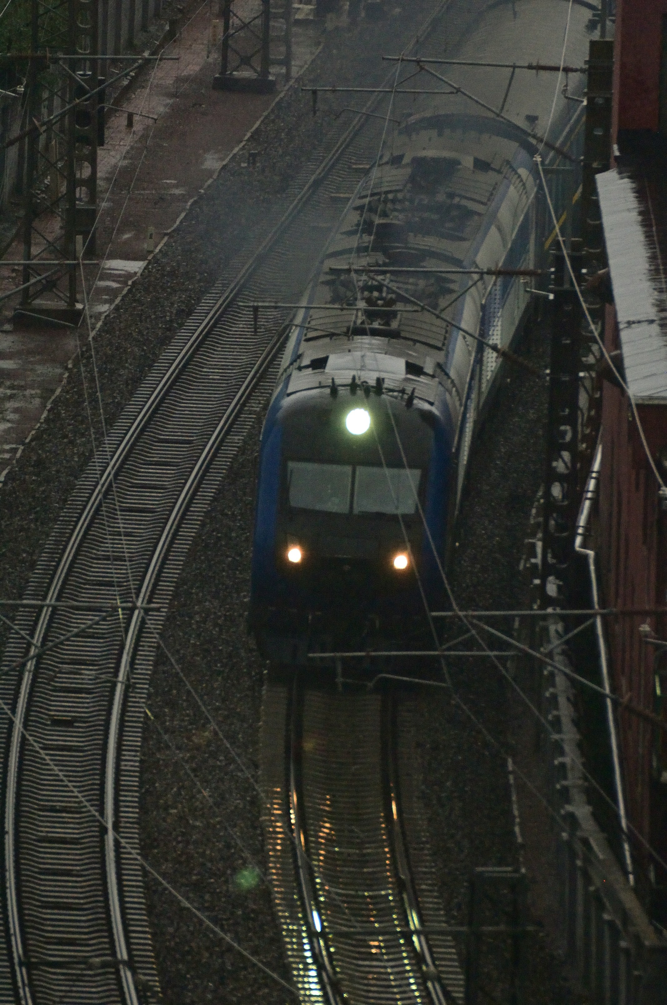 A blue train traveling down train tracks next to a building photo ...