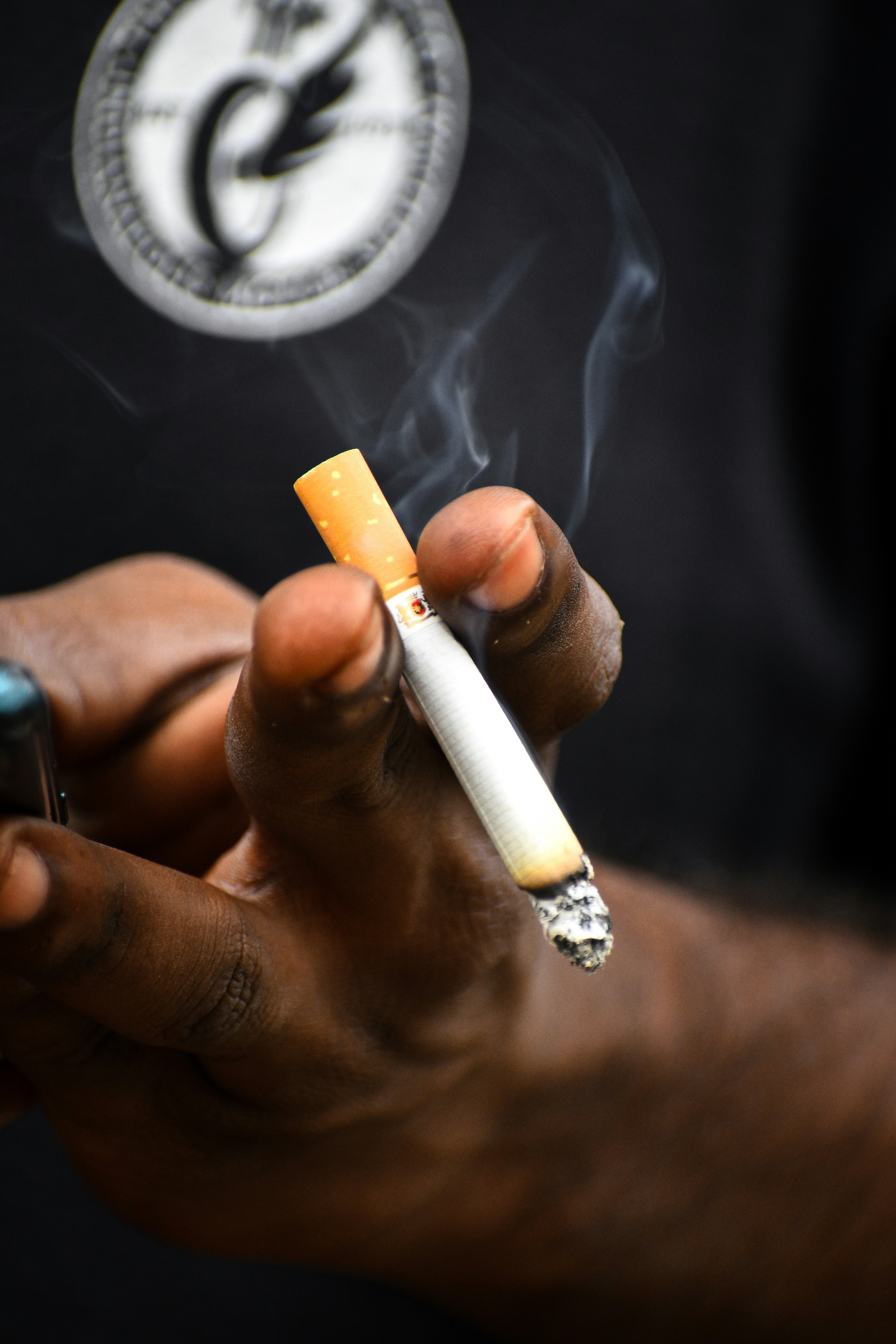 Cigarette Pinch: Close-Up of Smoke and Shadow with a Blurred Emblem