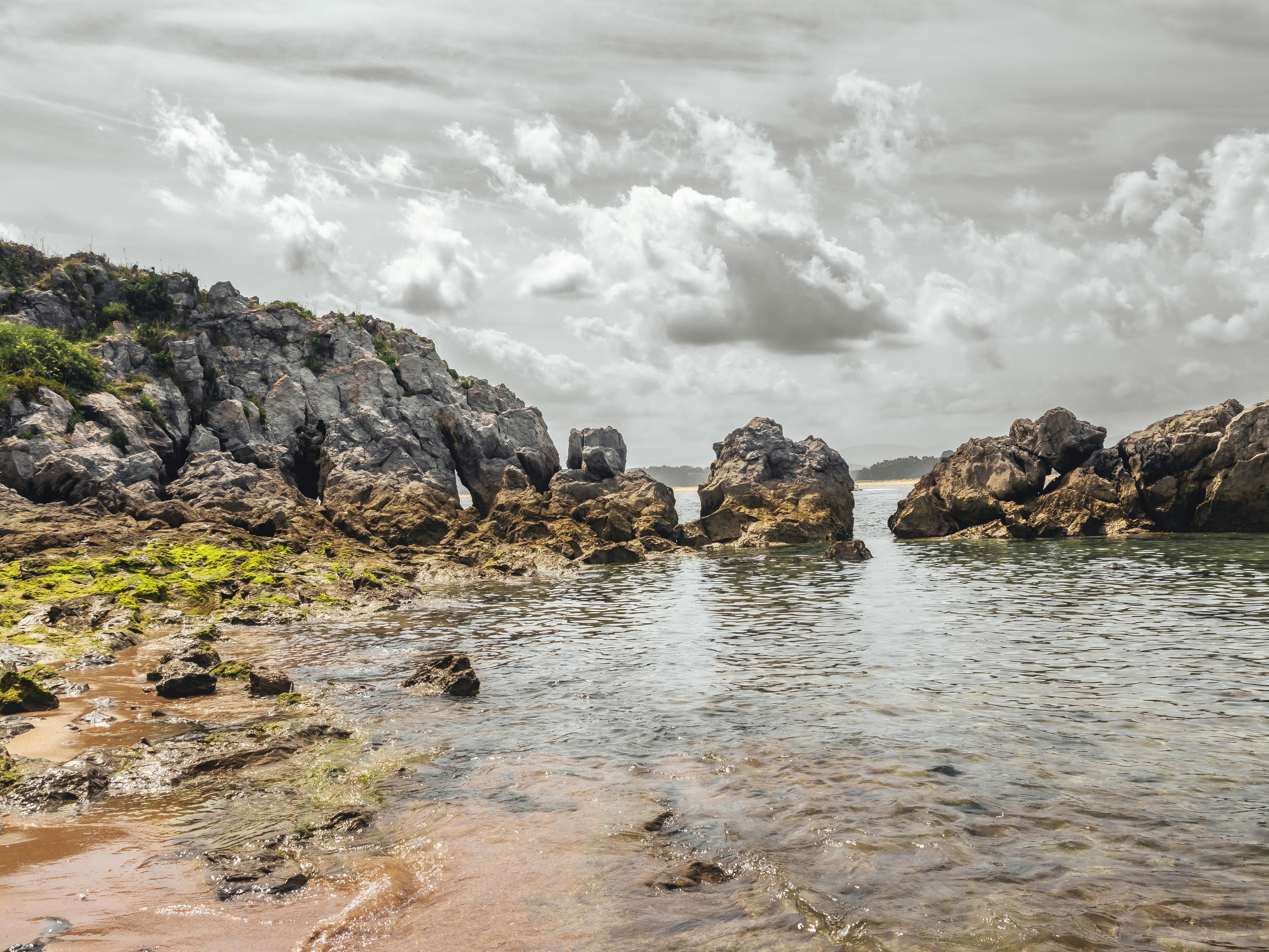 A body of water surrounded by rocks under a cloudy sky photo – Free ...