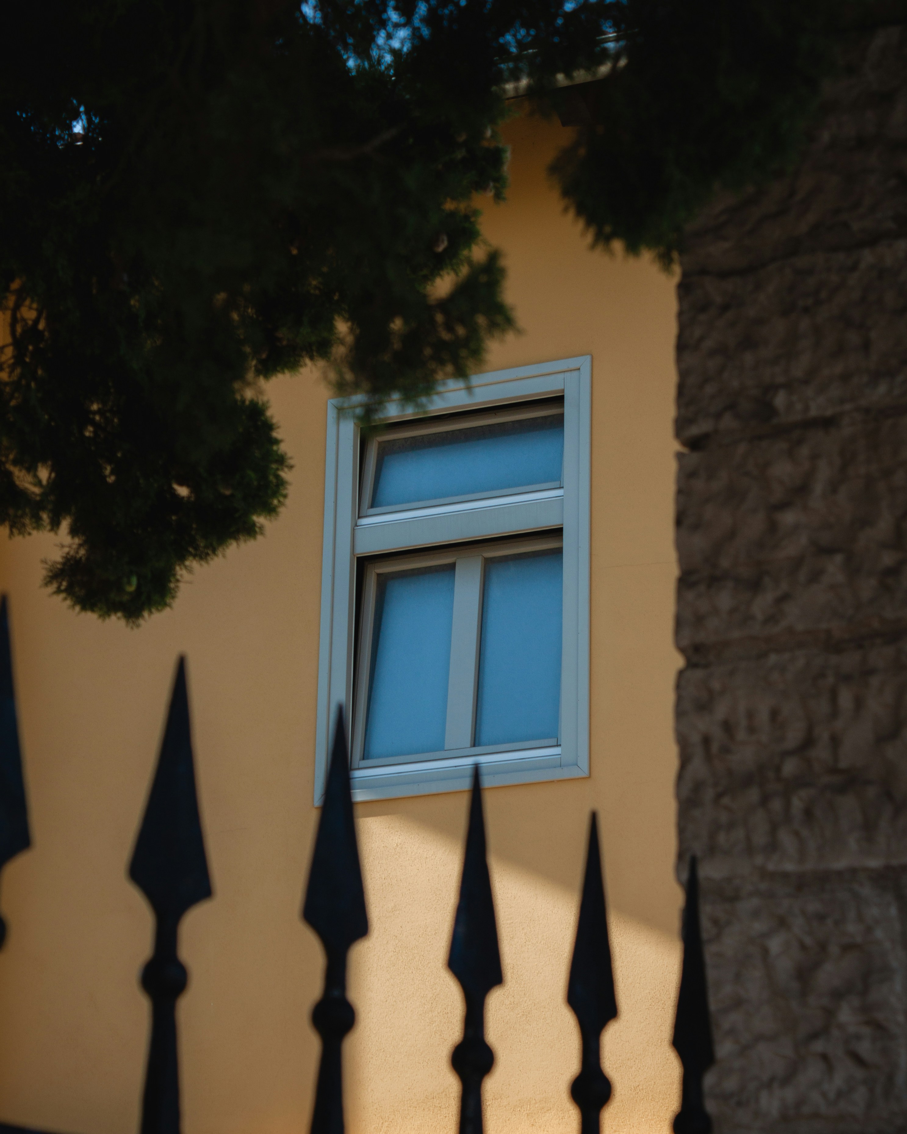 Azure Window on a Sunlit Yellow Wall Framed by Iron Spikes