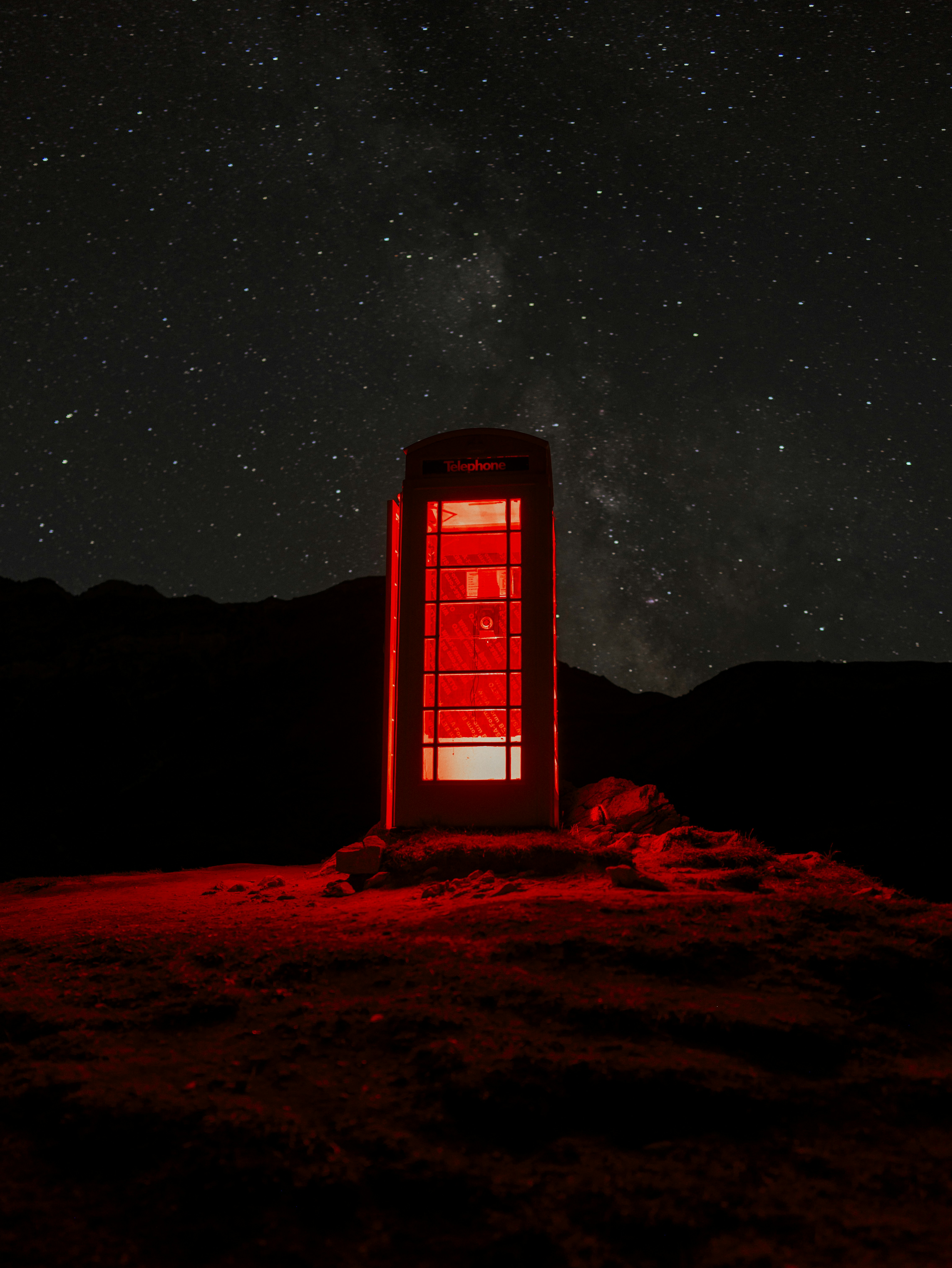 A red phone booth sitting on top of a hill under a night sky photo ...