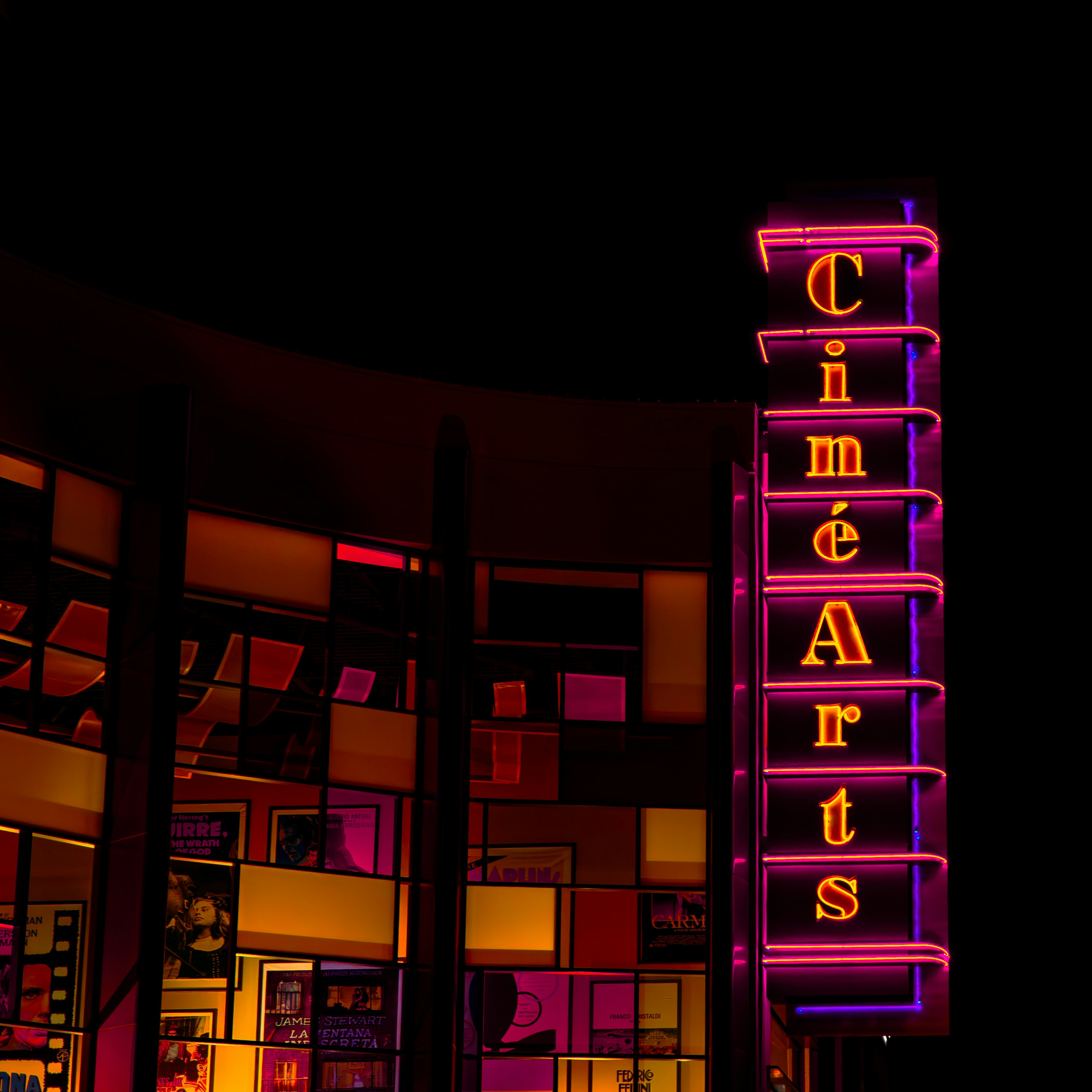 Neon vertical sign of CinéArts glows along a theater facade at night