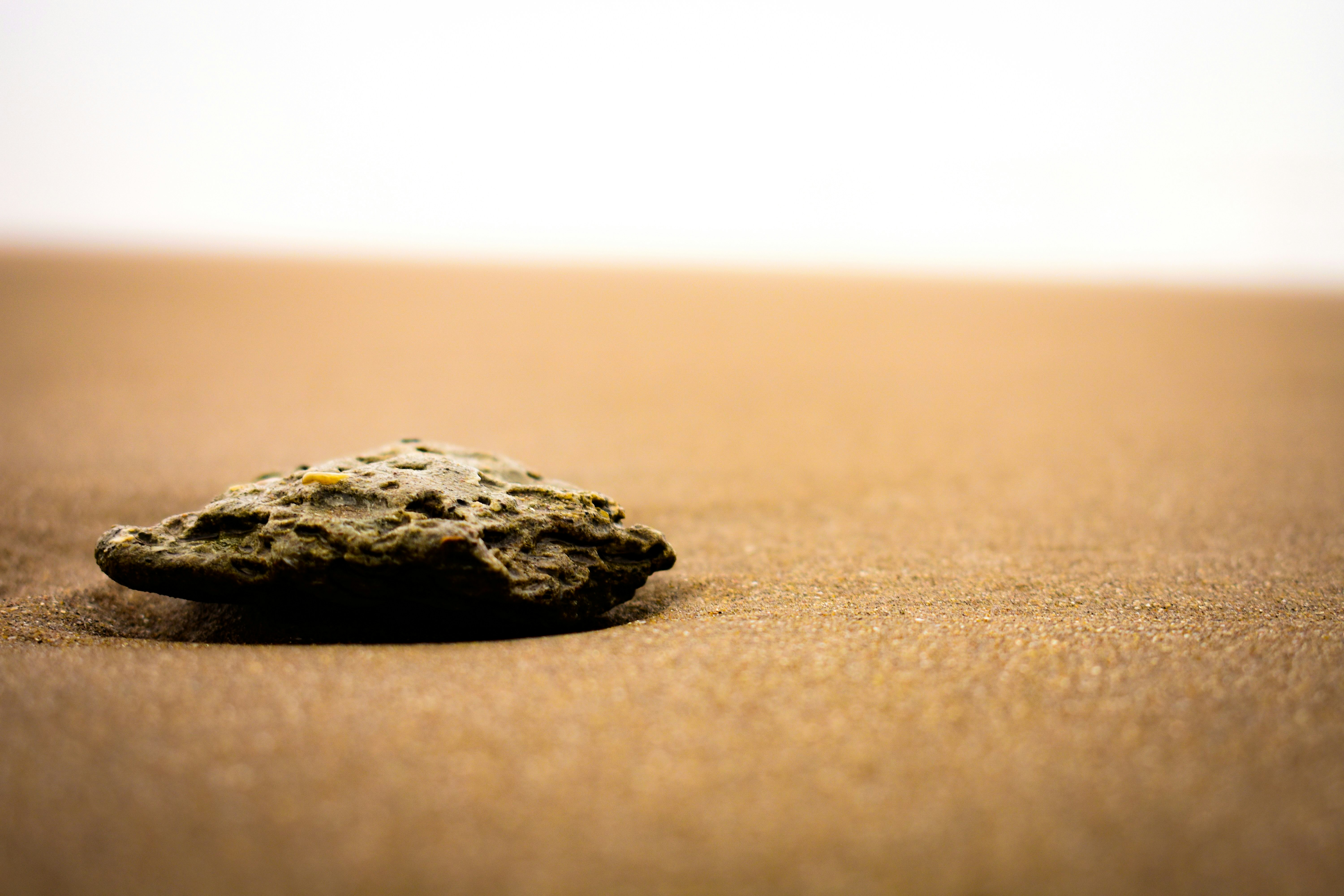 Single rock resting on a sandy surface under a bright sky.