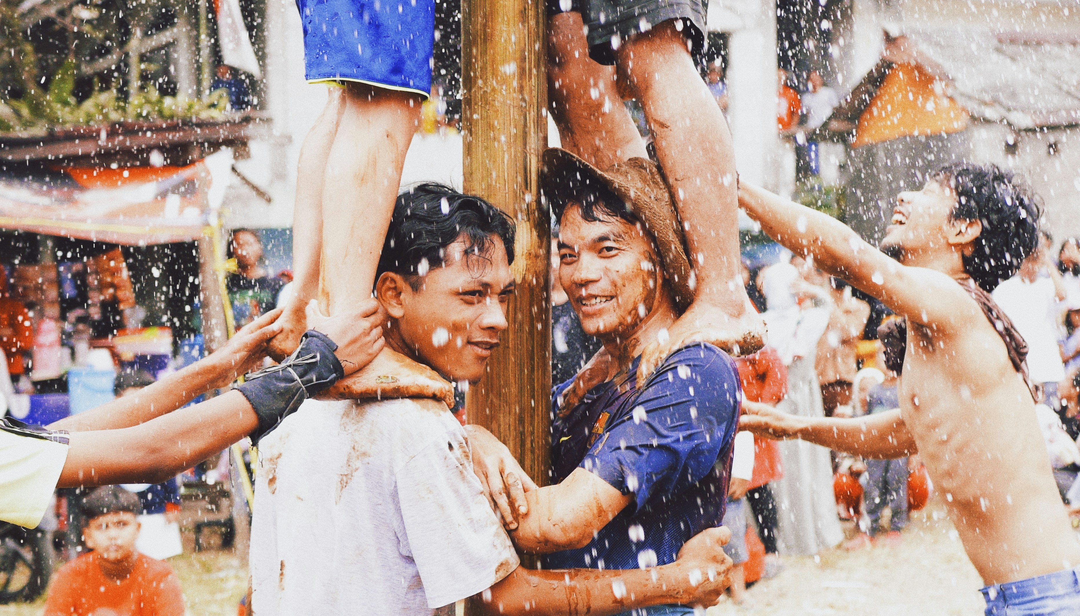 Joyful group of kids clings to a wooden pole as water sprays around them. A candid outdoor moment capturing playful energy and friendship amid a busy splash scene.