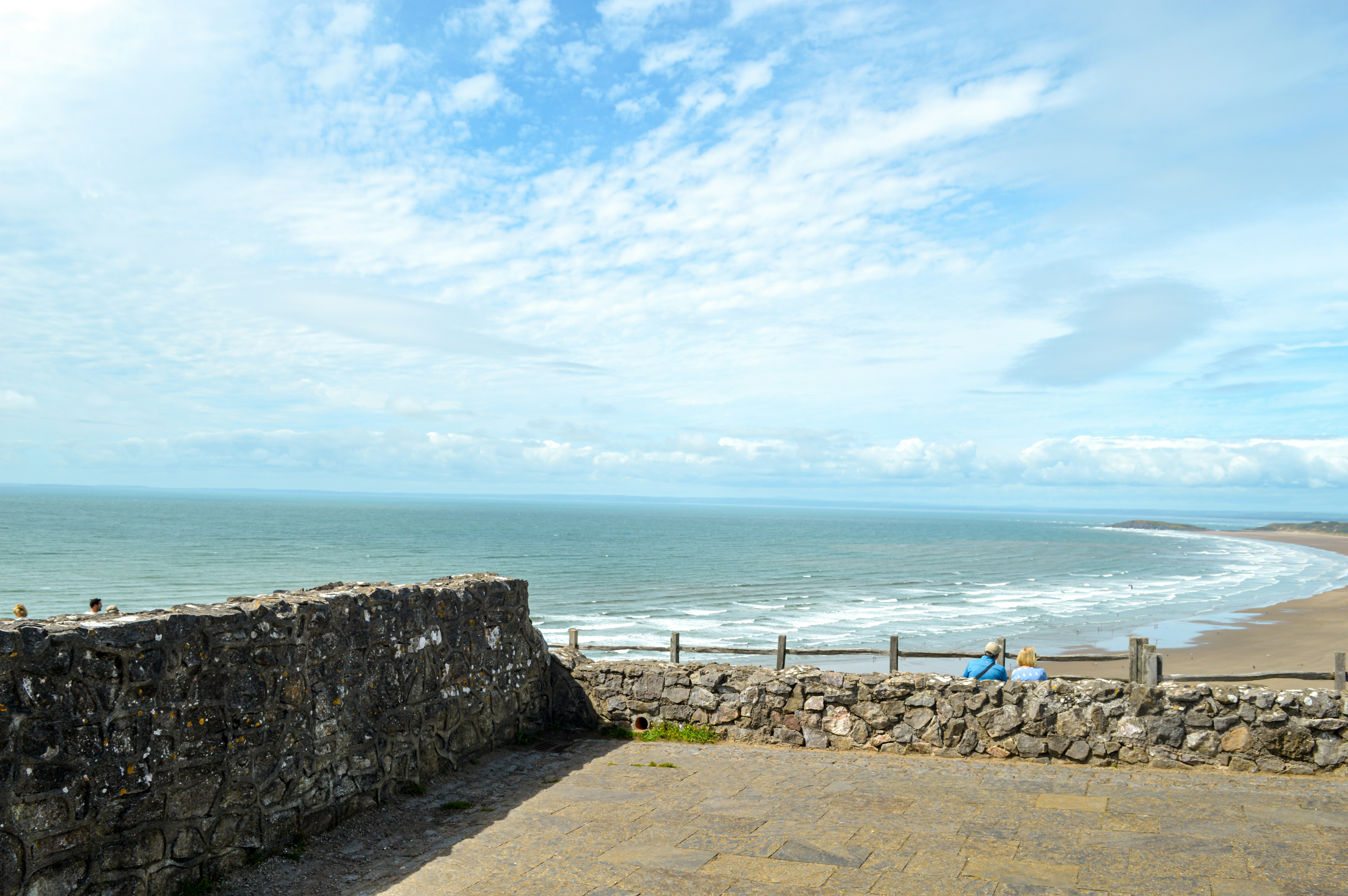 A stone wall next to the ocean with people sitting on it photo – Free ...